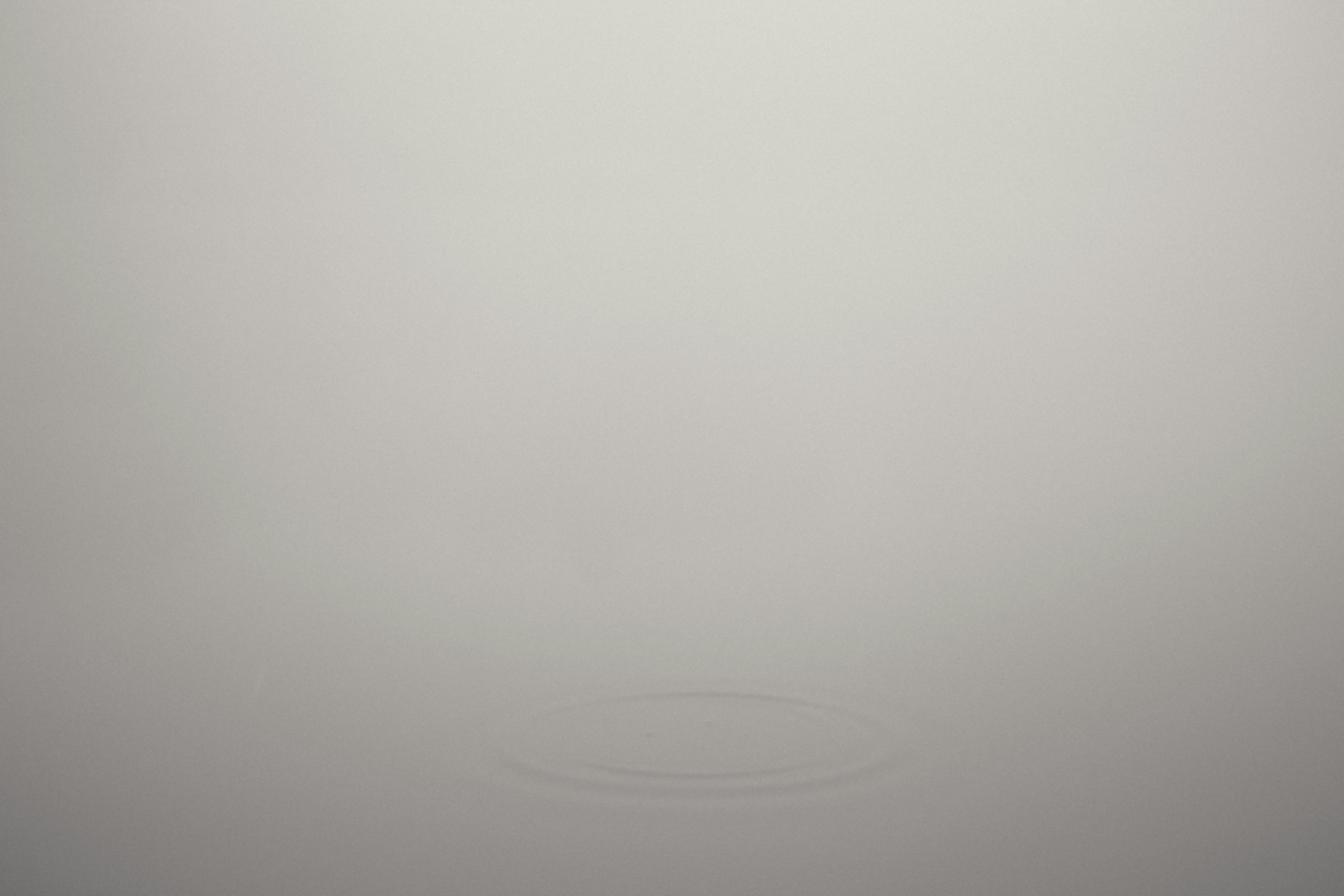 A subtle ripple spreads across a calm surface, enveloped in a soft, foggy atmosphere. The simplicity evokes a sense of tranquility.