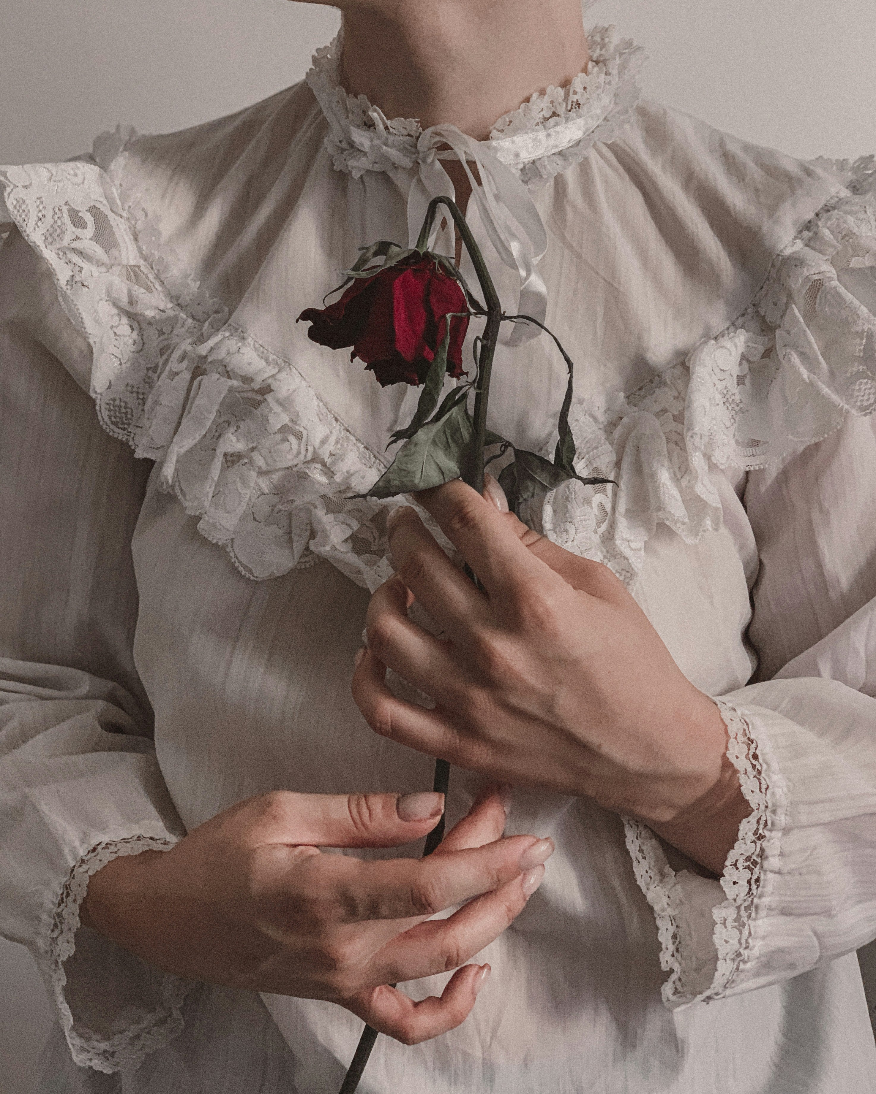 Delicate hands hold a wilted rose, adorned in a vintage lace blouse, evoking a sense of nostalgia and fragility.