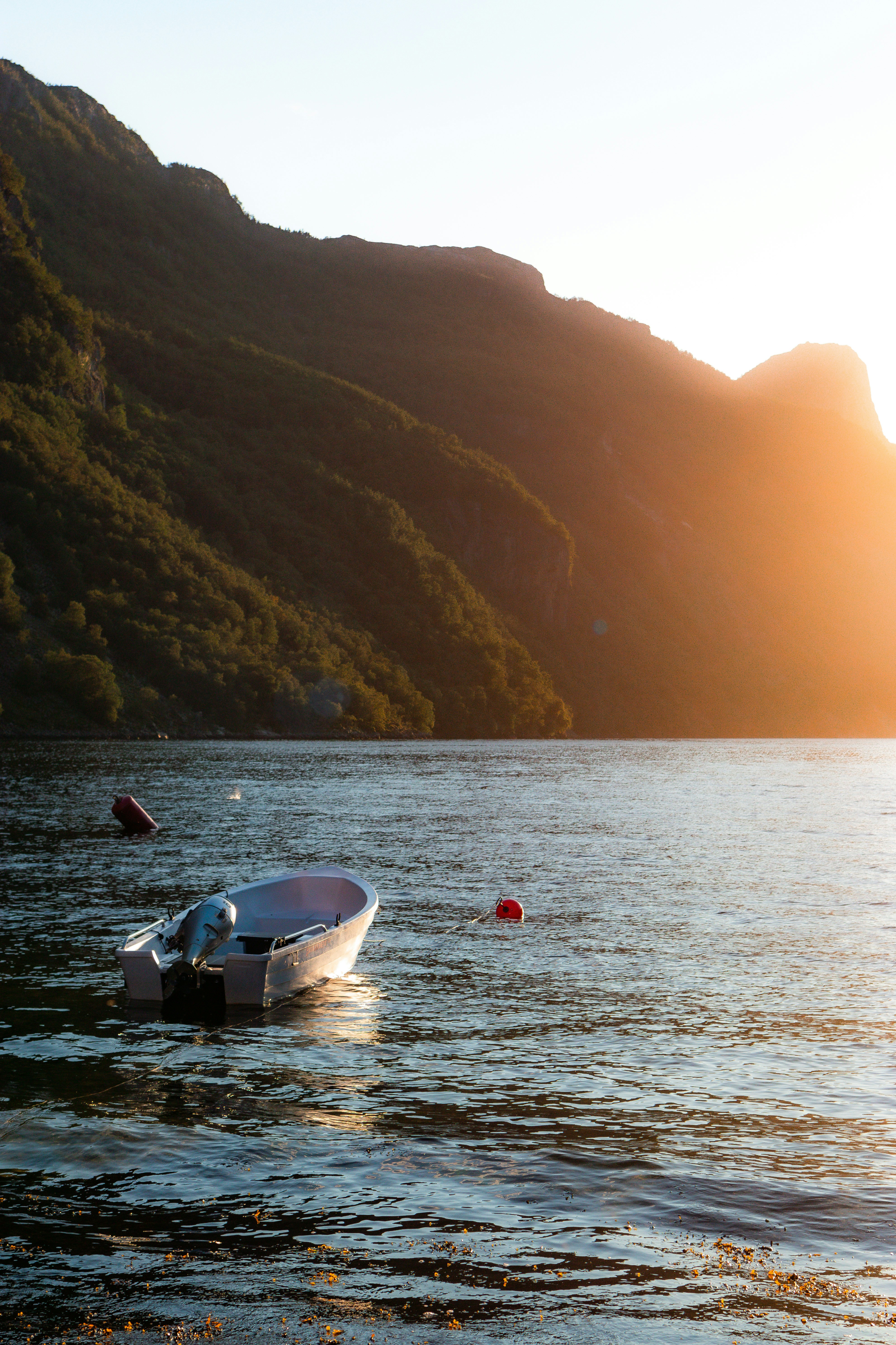 Small boat floating in a sunlit fjord with mountainous silhouettes at sunset.