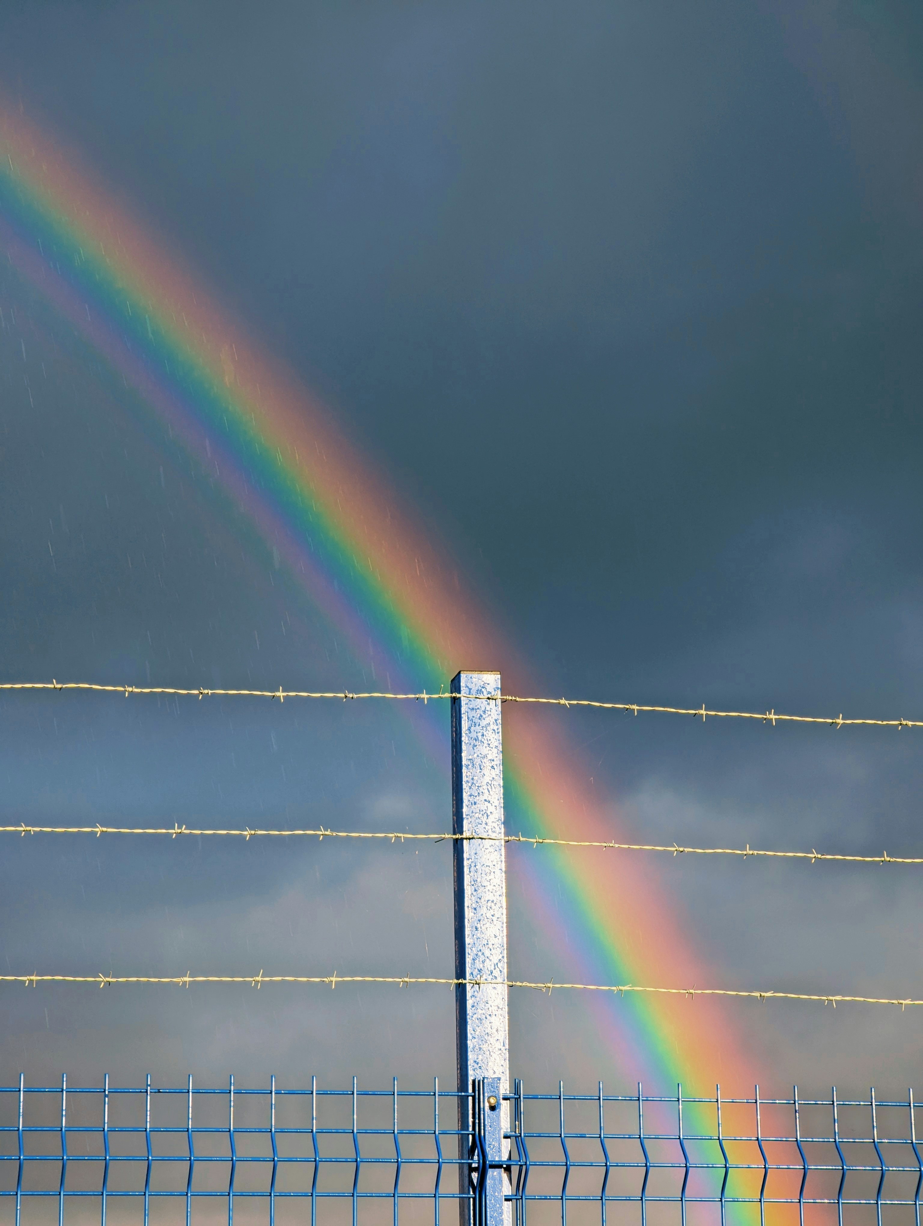Rainbow Arch Over a Weathered Fence