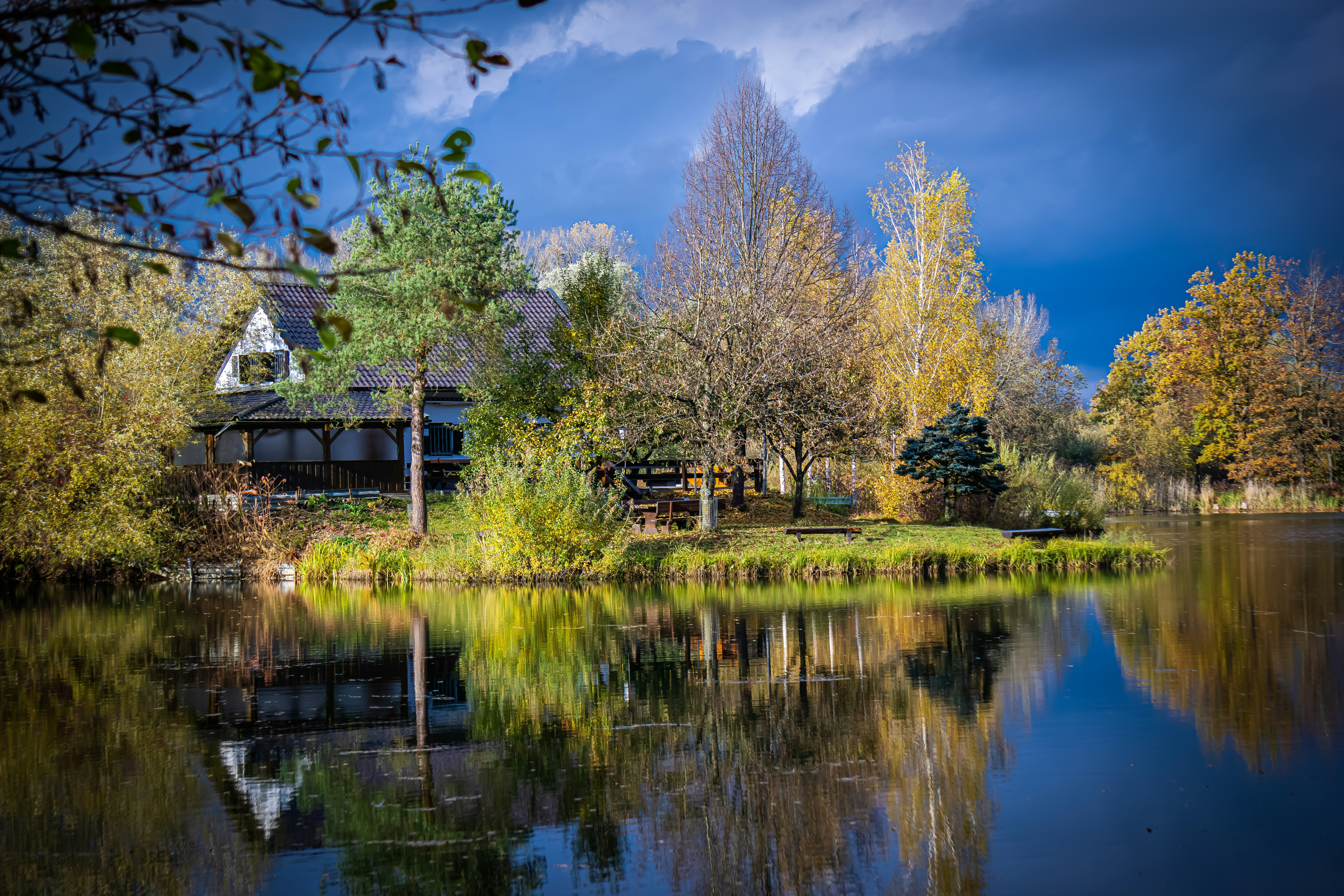 A picturesque lakeside view featuring a charming house surrounded by autumn foliage, with vibrant reflections mirrored in the calm water.