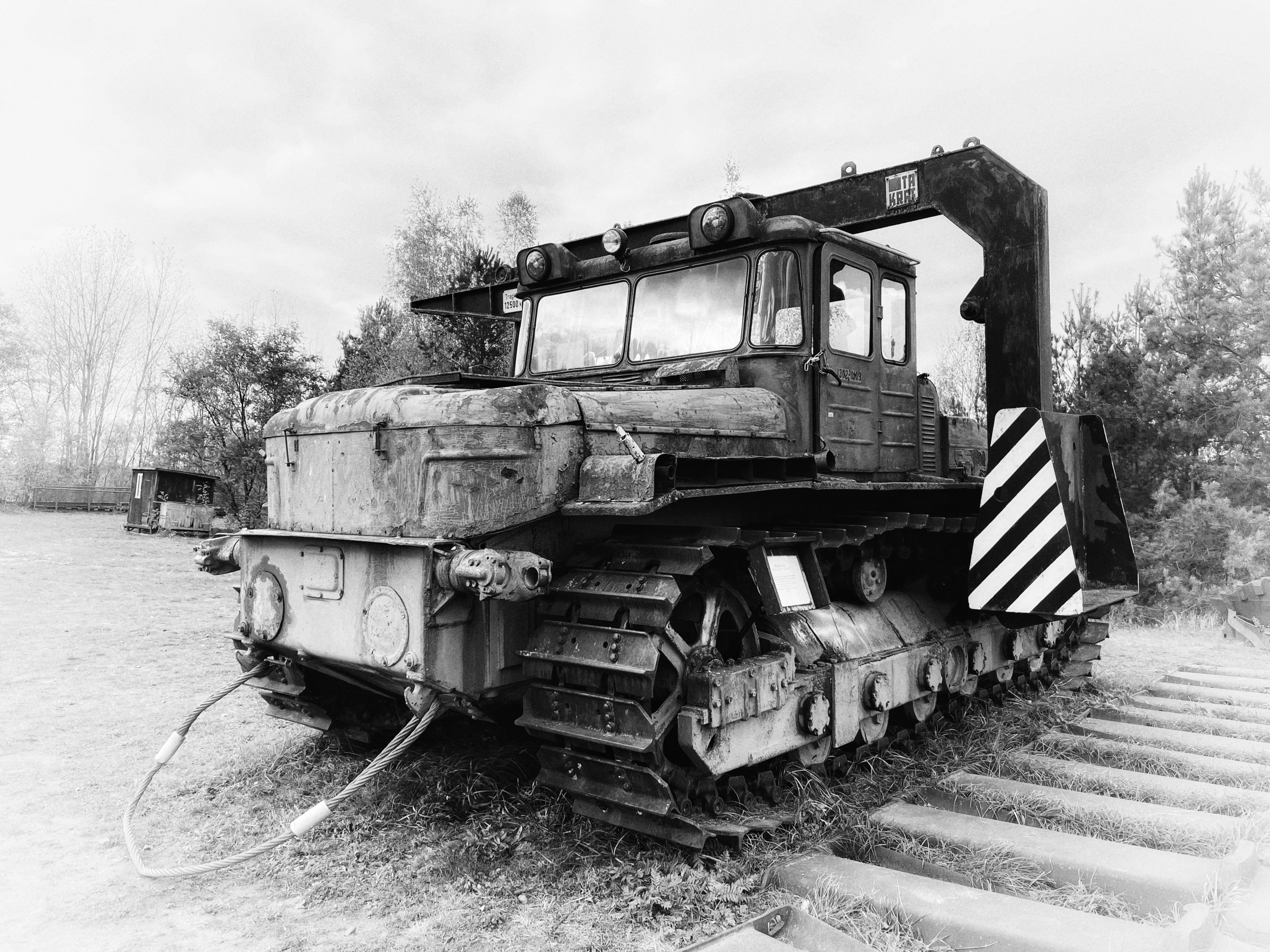 An abandoned, weathered excavator sits on tracks in a desolate landscape, showcasing its rugged design and faded paint. The scene captures the essence of industrial decay.