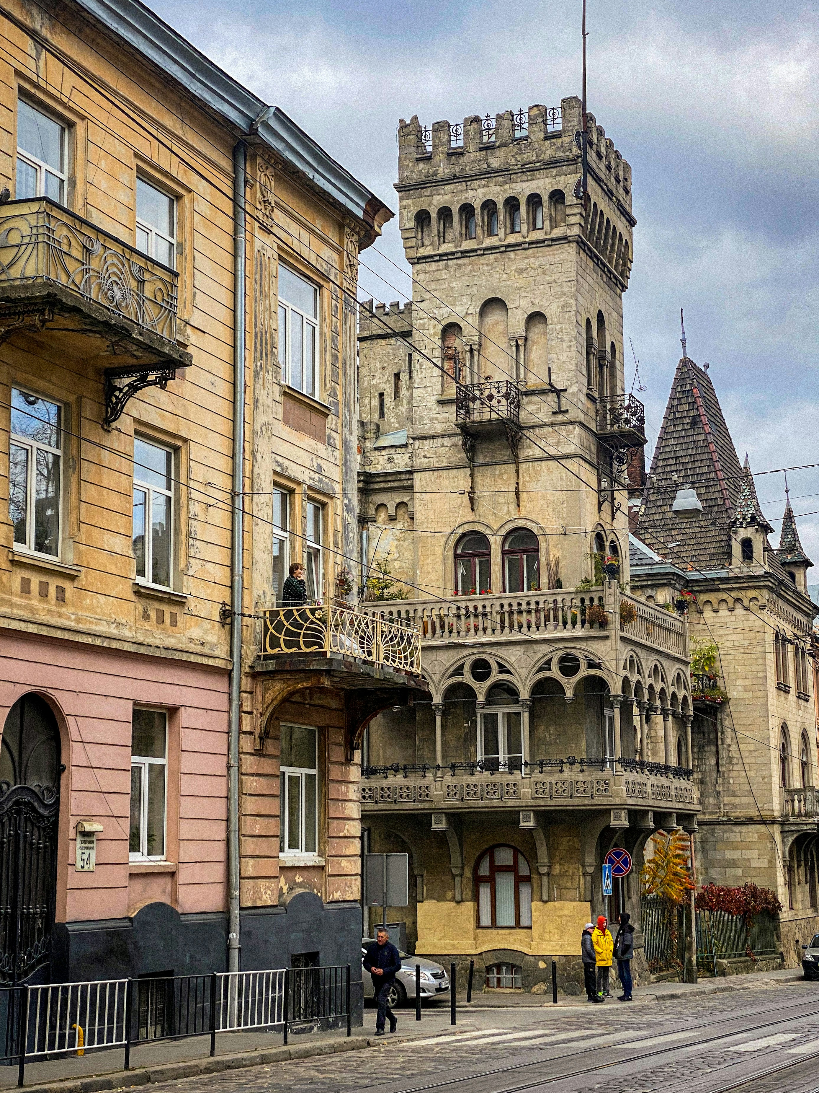 Intricate facades of historic buildings line a cobblestone street, showcasing a blend of styles and textures. People stroll by, adding life to the architectural narrative.