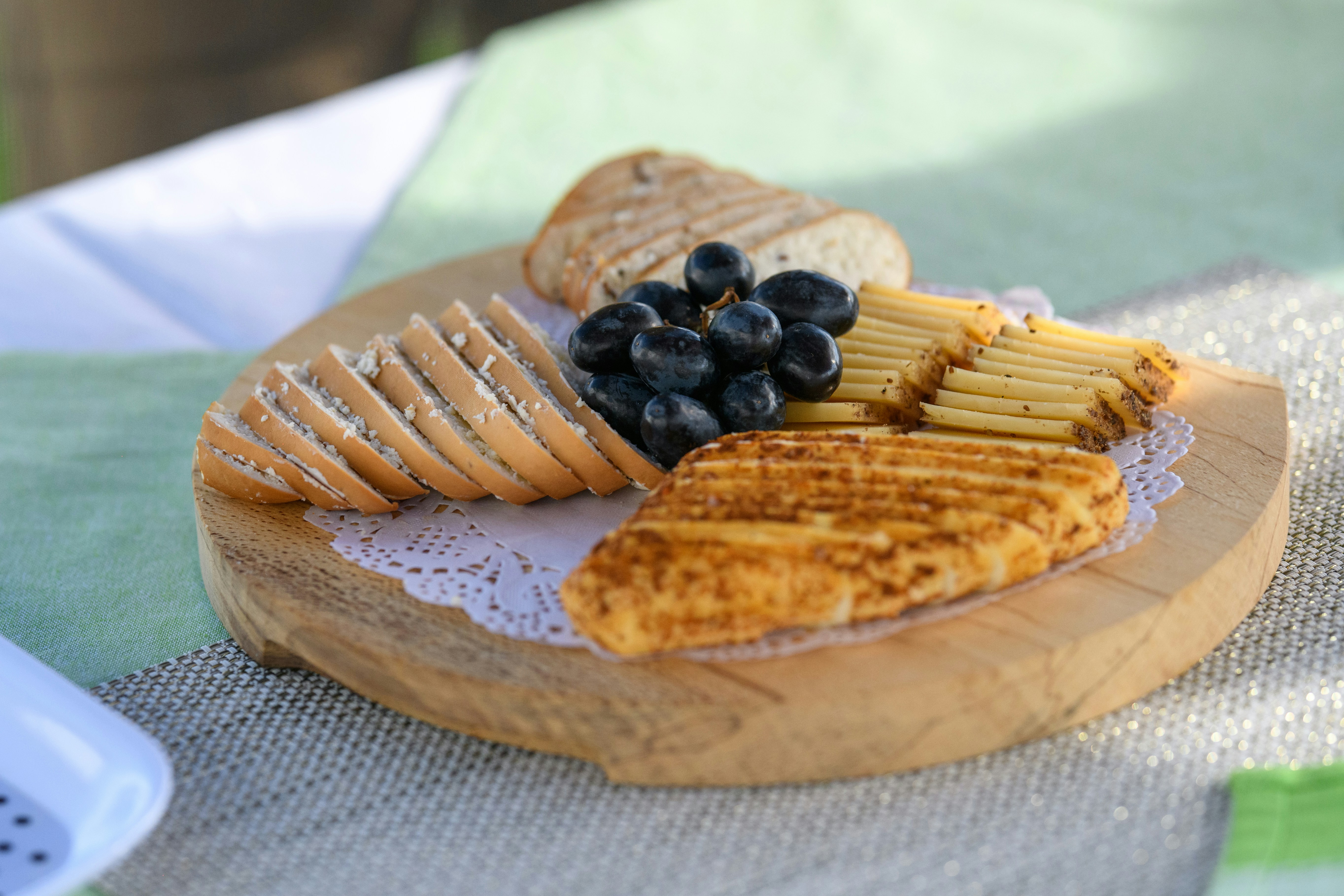 An assortment of cheeses and crackers elegantly arranged on a wooden platter, accompanied by fresh blueberries, set against a soft green backdrop.