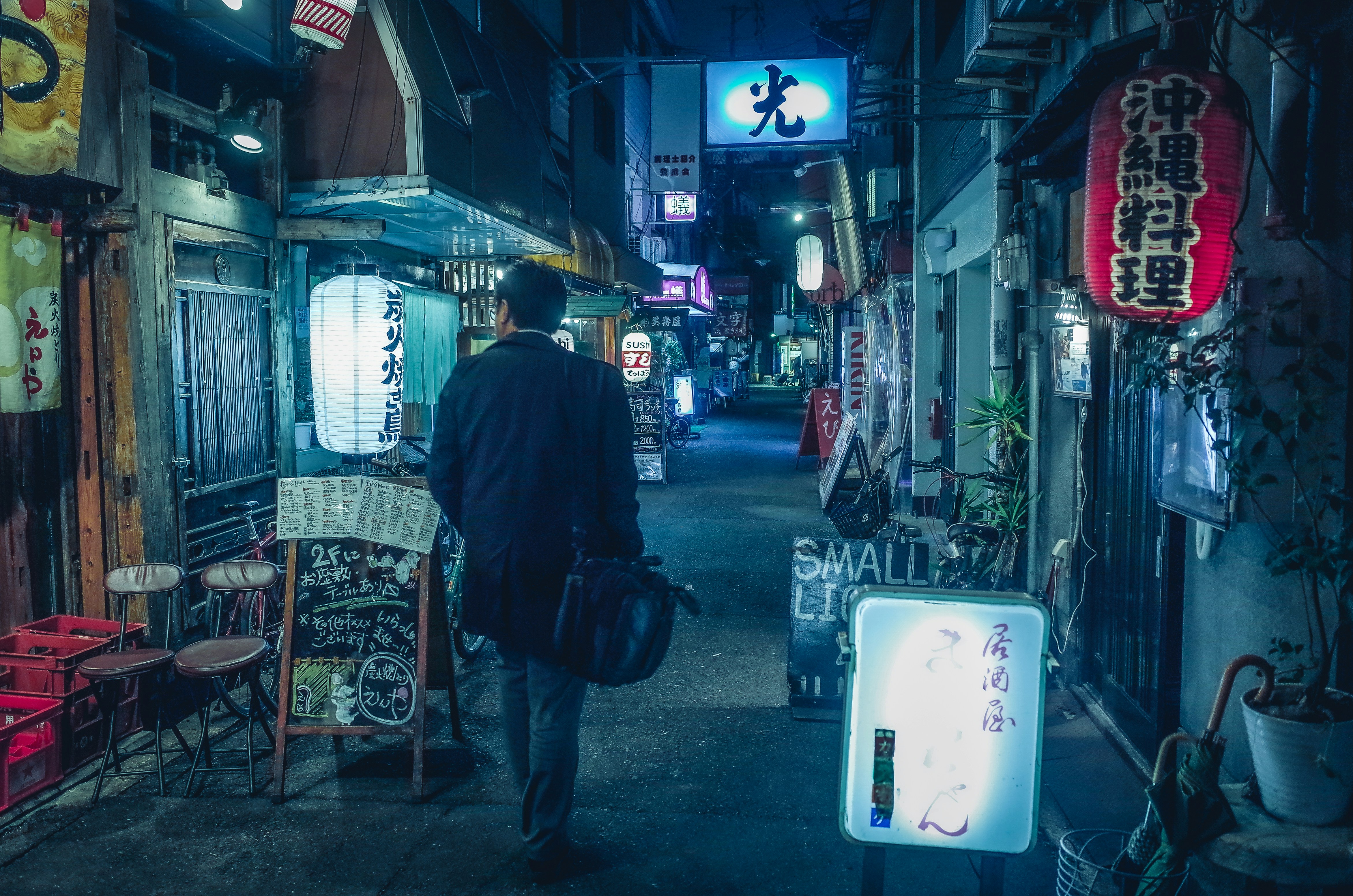 Night street photograph of a man in a suit walking away down a neon-lit alley lined with signs.