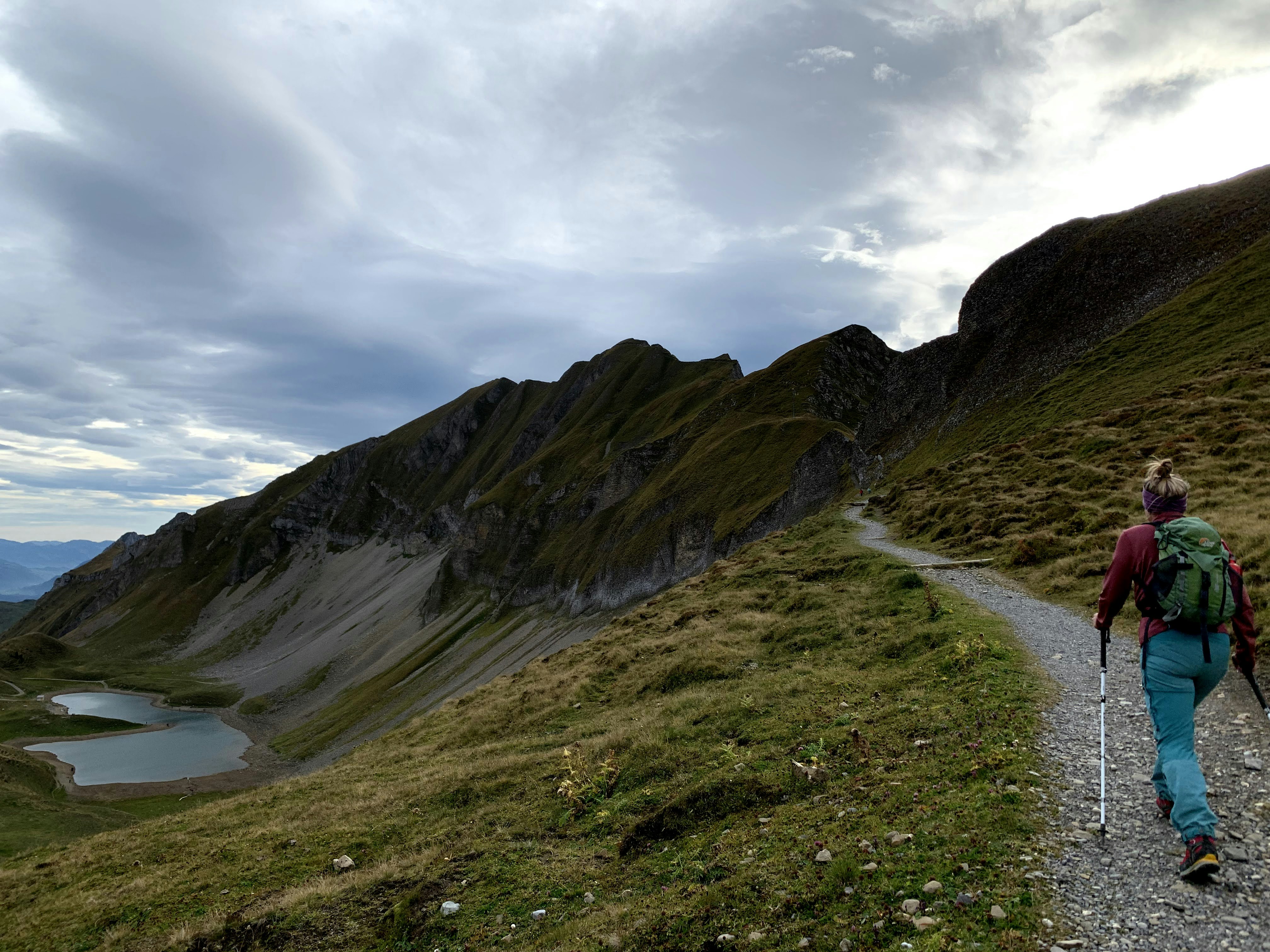 Ridgebound Trek: The lone hiker threading a wind-swept path above a glacial lake