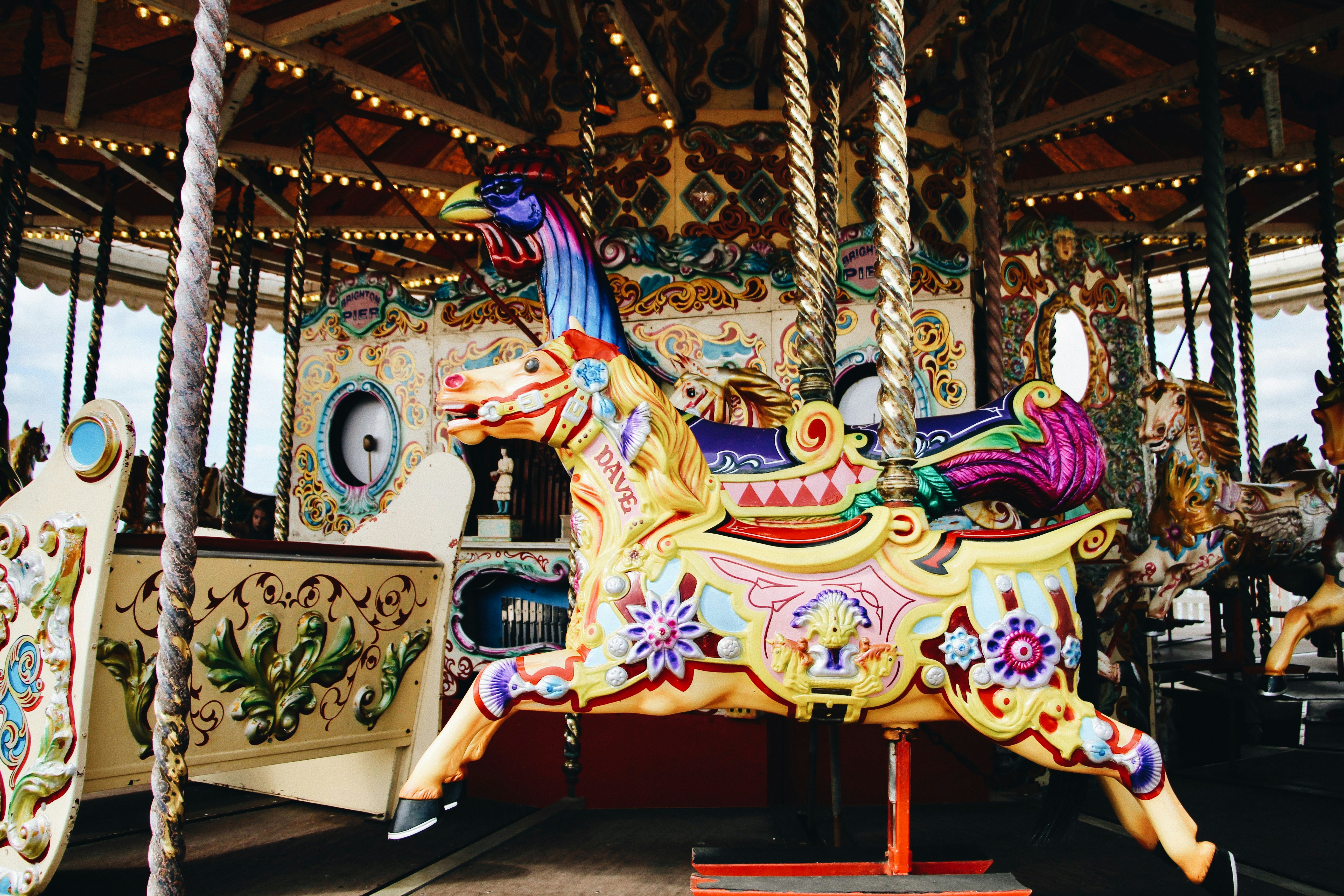 Vibrantly painted carousel horse in motion, surrounded by ornate decorations and lights. The scene evokes a sense of nostalgia and joy.