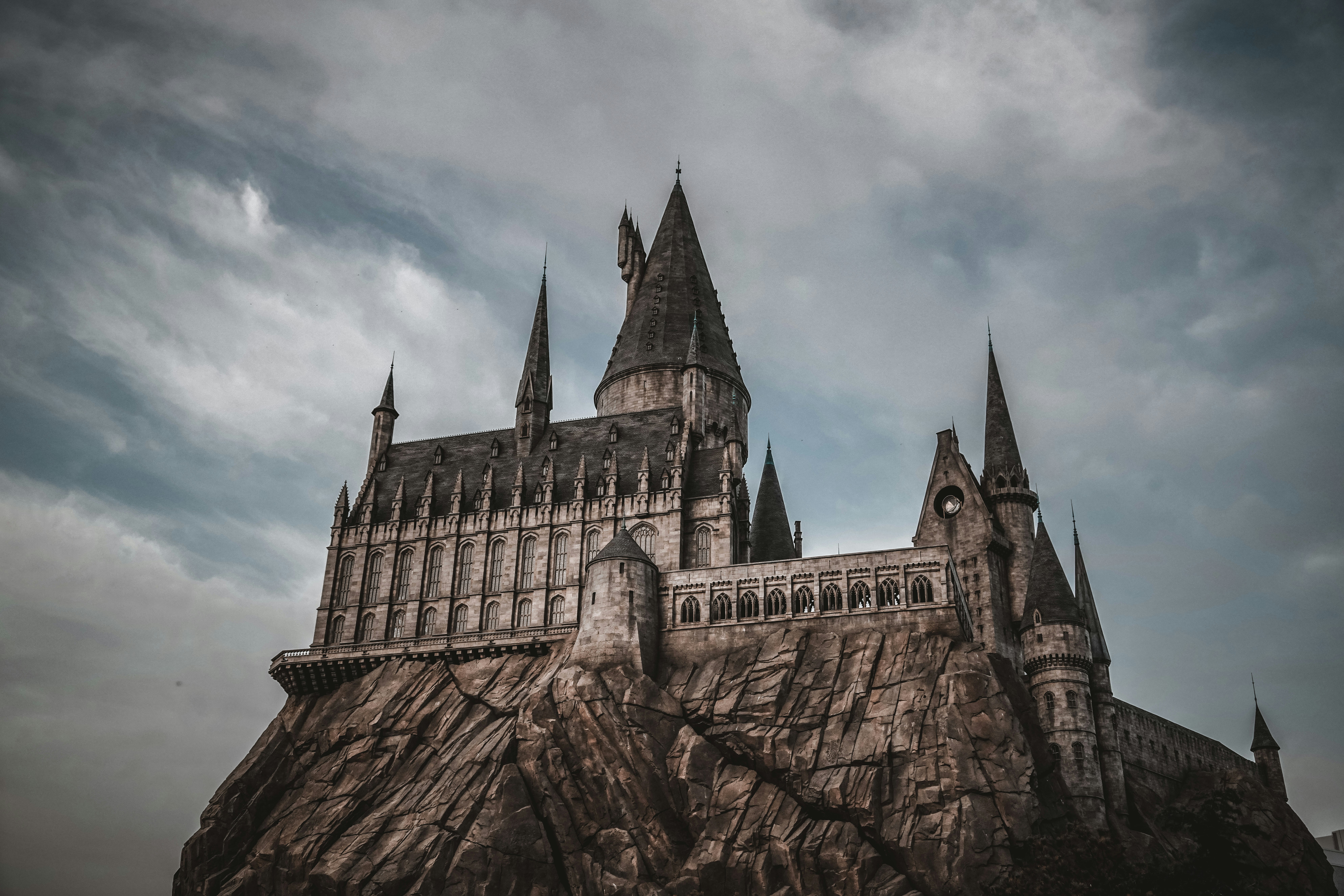 Majestic castle perched atop a rocky cliff under a moody sky, showcasing intricate architectural details and towering spires.