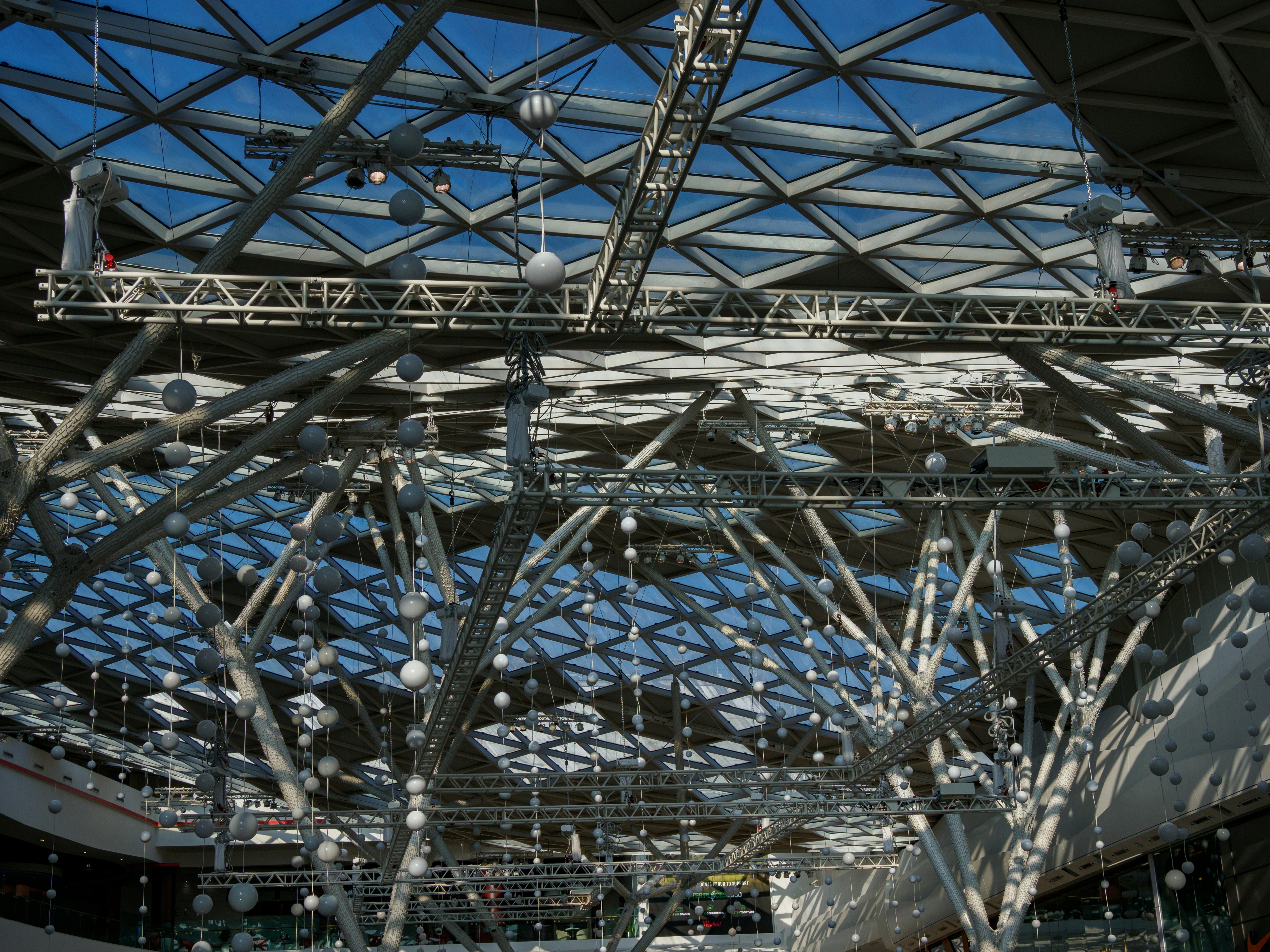 Intricate lattice of beams and suspended lights beneath a glass ceiling, showcasing modern architectural design.