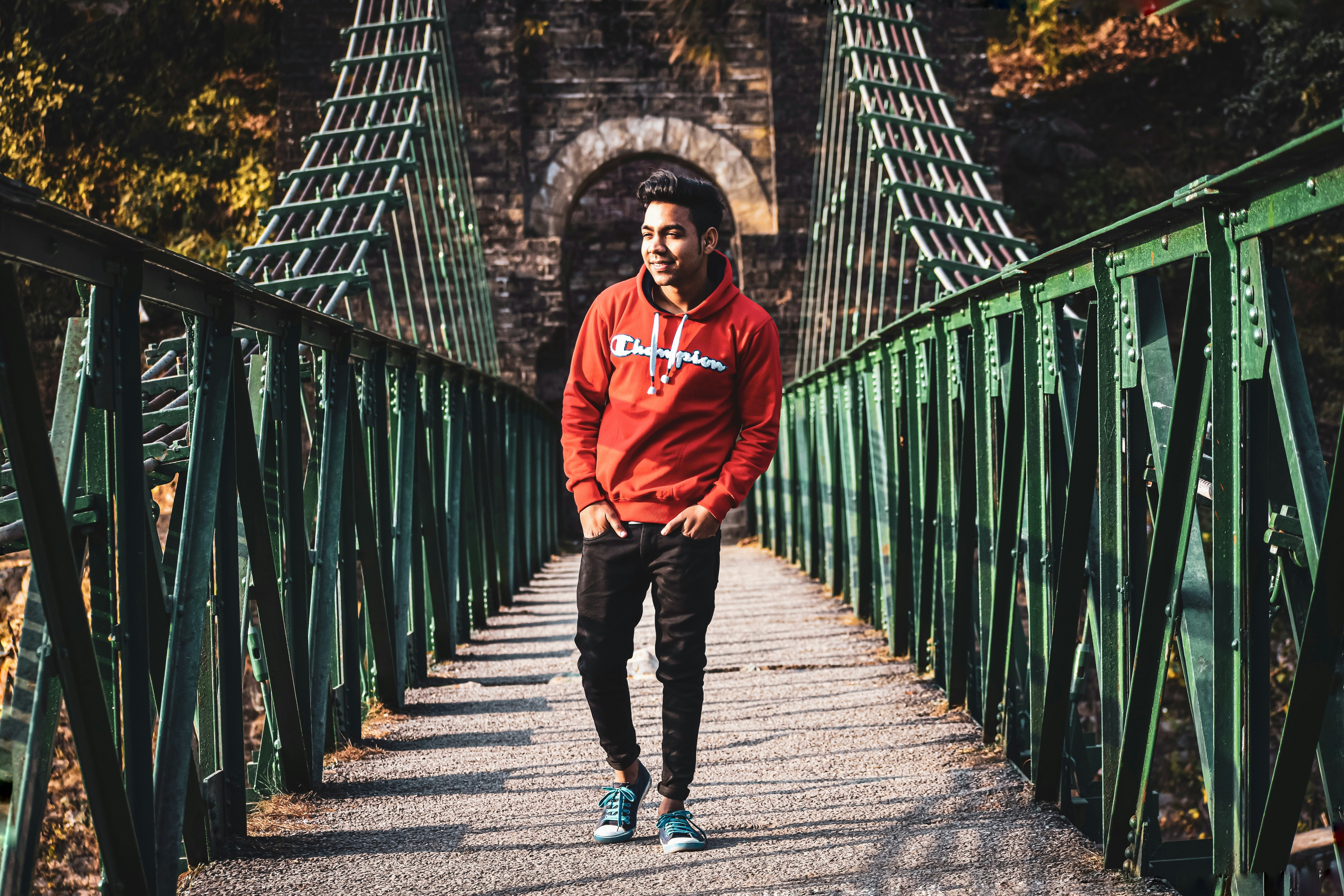 Man in a red sweatshirt walking on a green metal bridge surrounded by autumn foliage.