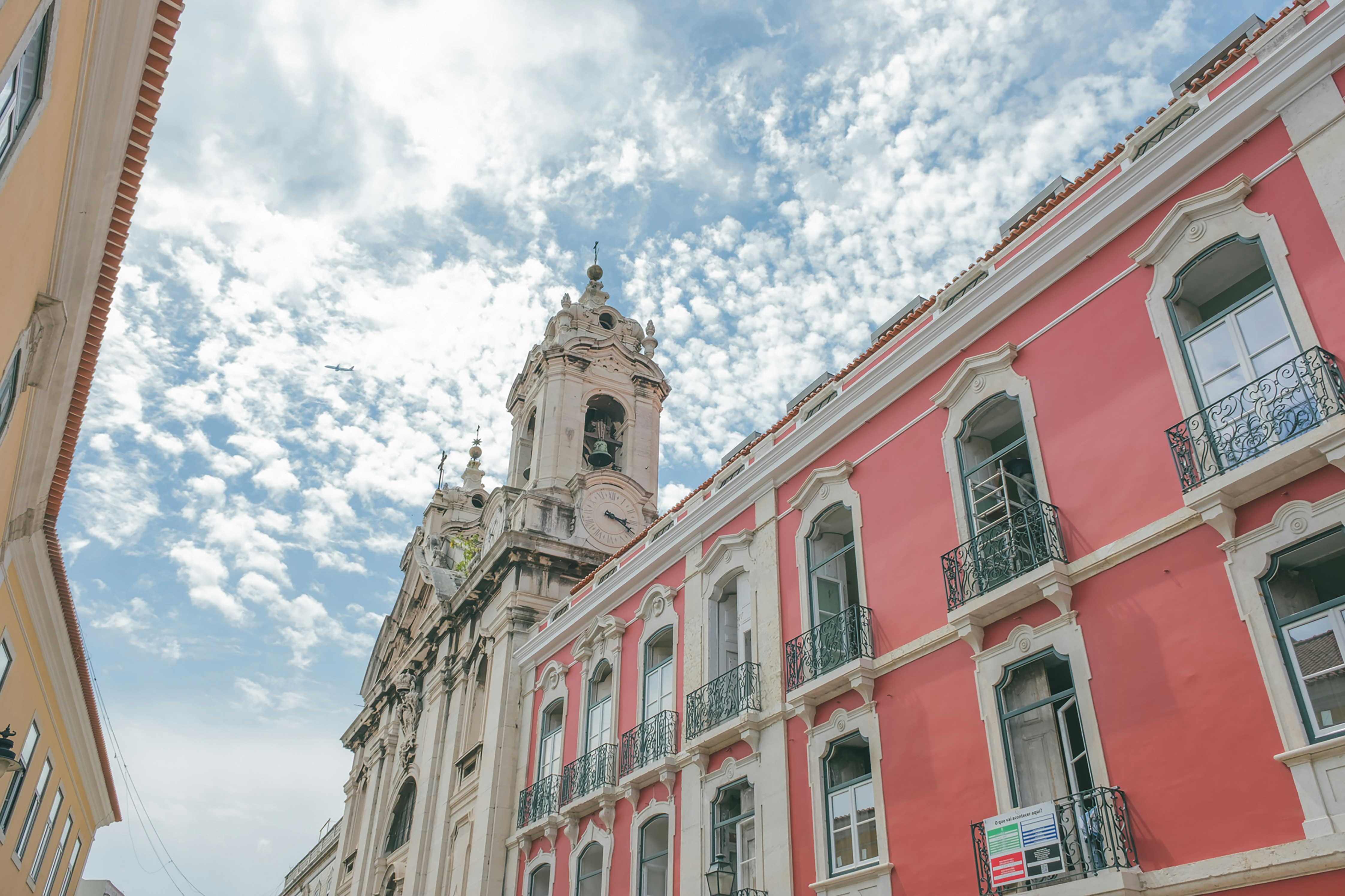 Ornate church tower rises beside a vibrant red building under a sky dotted with fluffy clouds.
