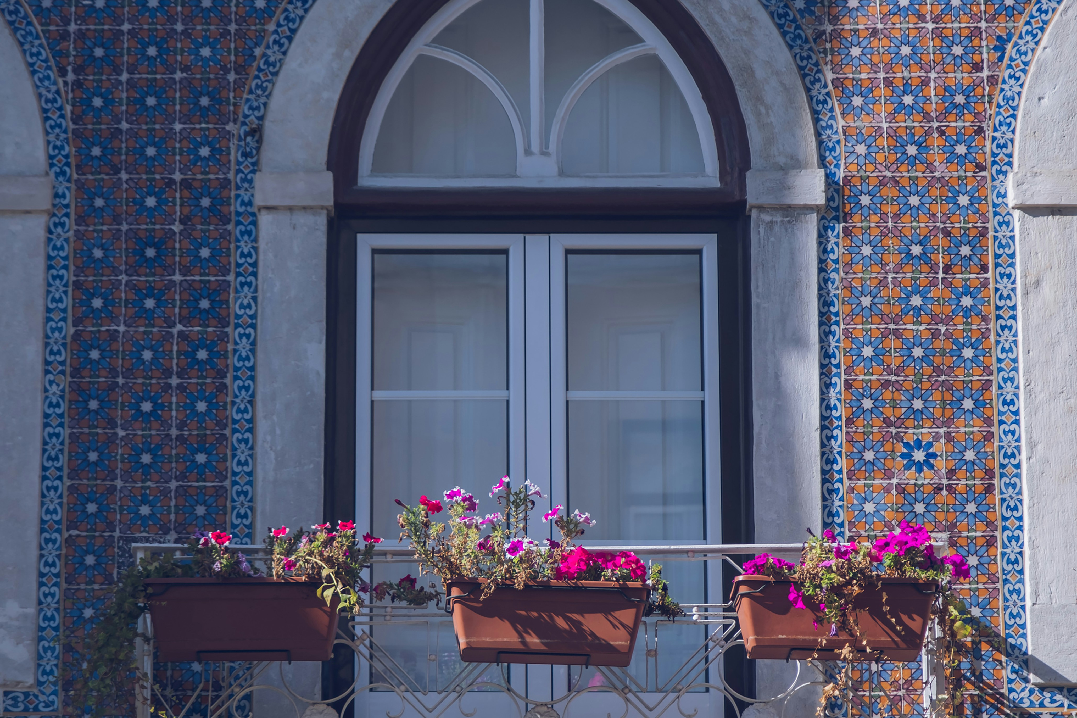 Arched window with colorful flower boxes against intricate blue and orange azulejo tiles.