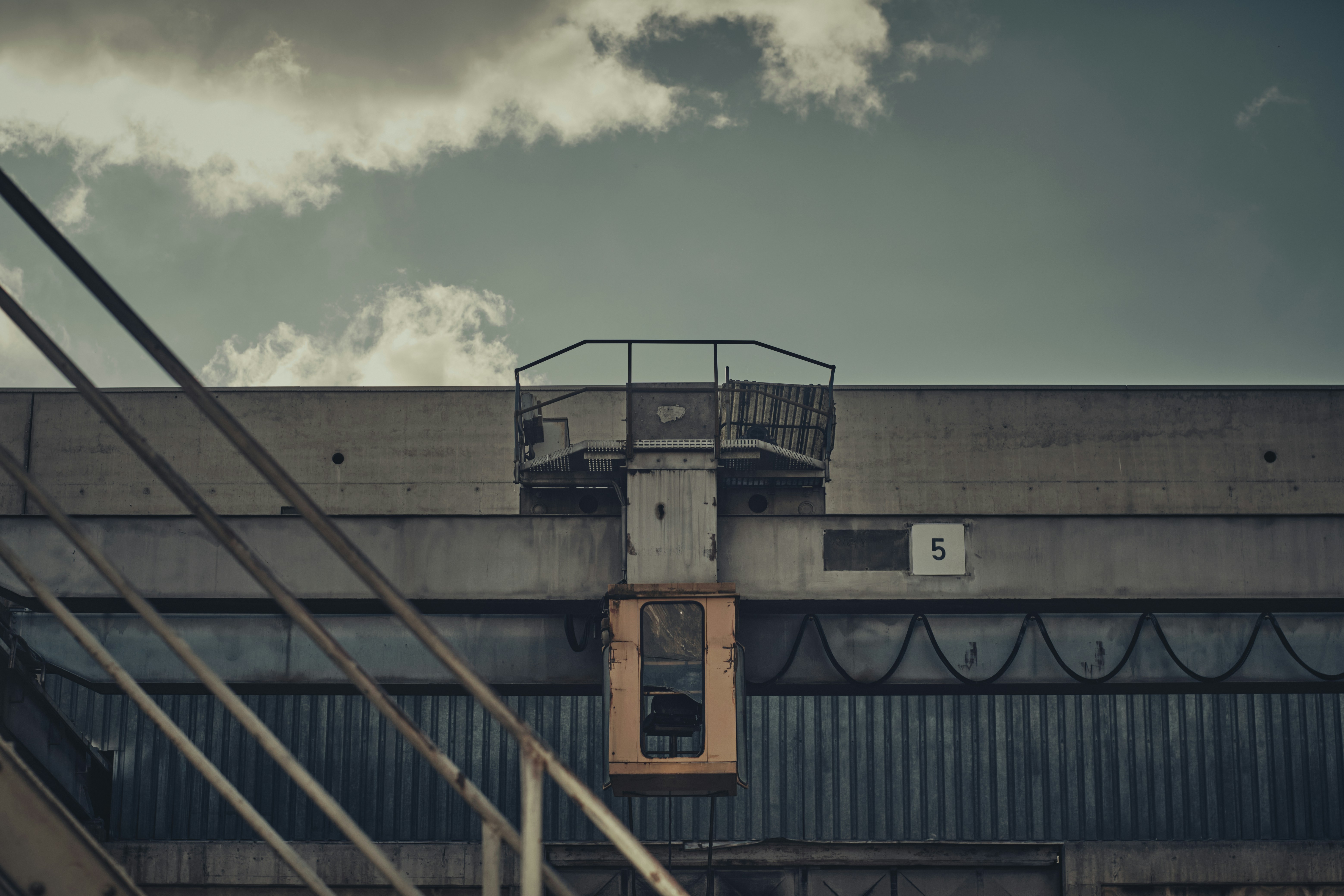 A weathered industrial control tower perched atop a concrete structure, framed by a moody sky. The scene captures the essence of urban machinery and architectural resilience.
