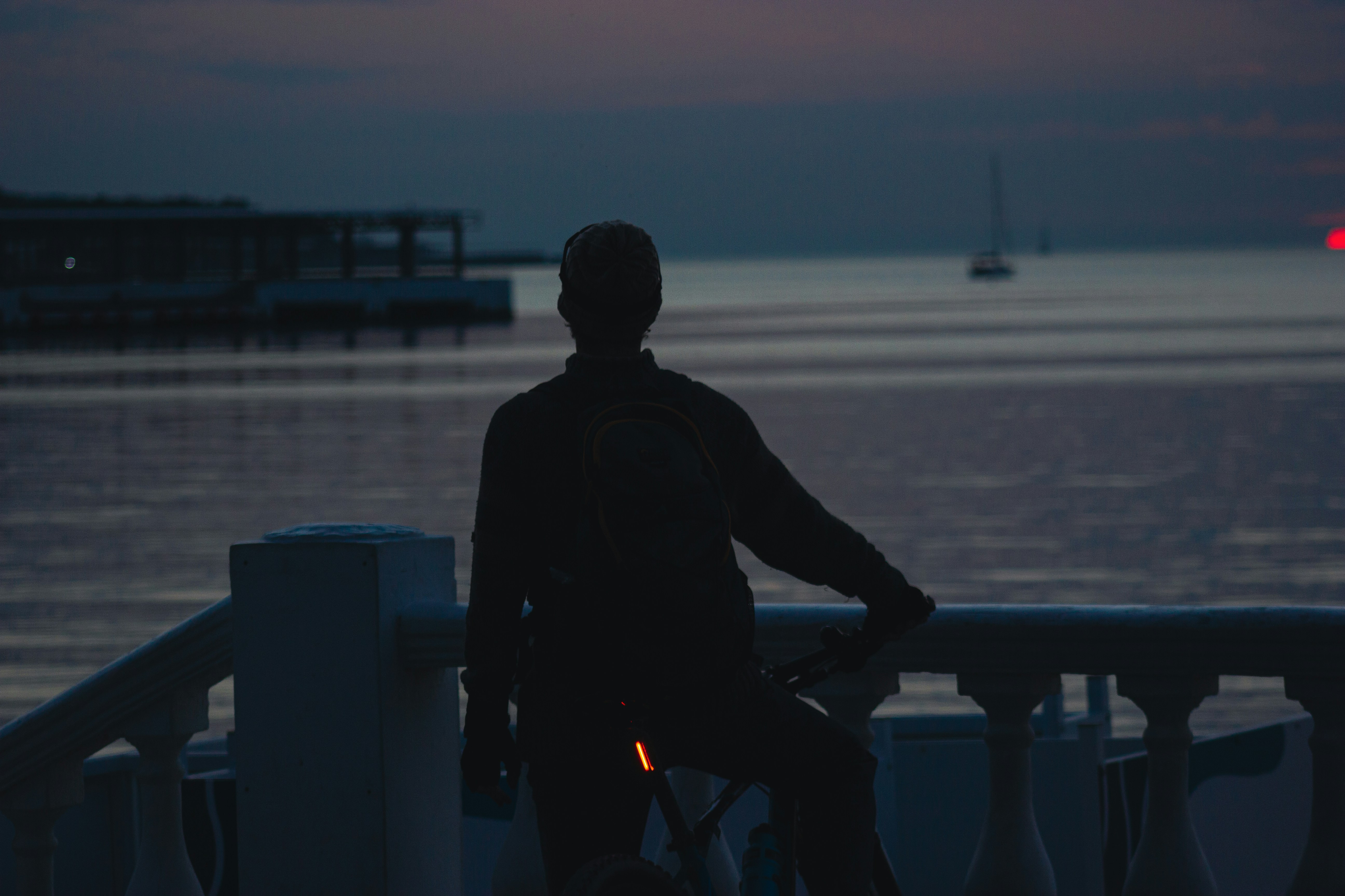 Silhouette at Dusk: A solitary figure gazes toward a quiet harbor