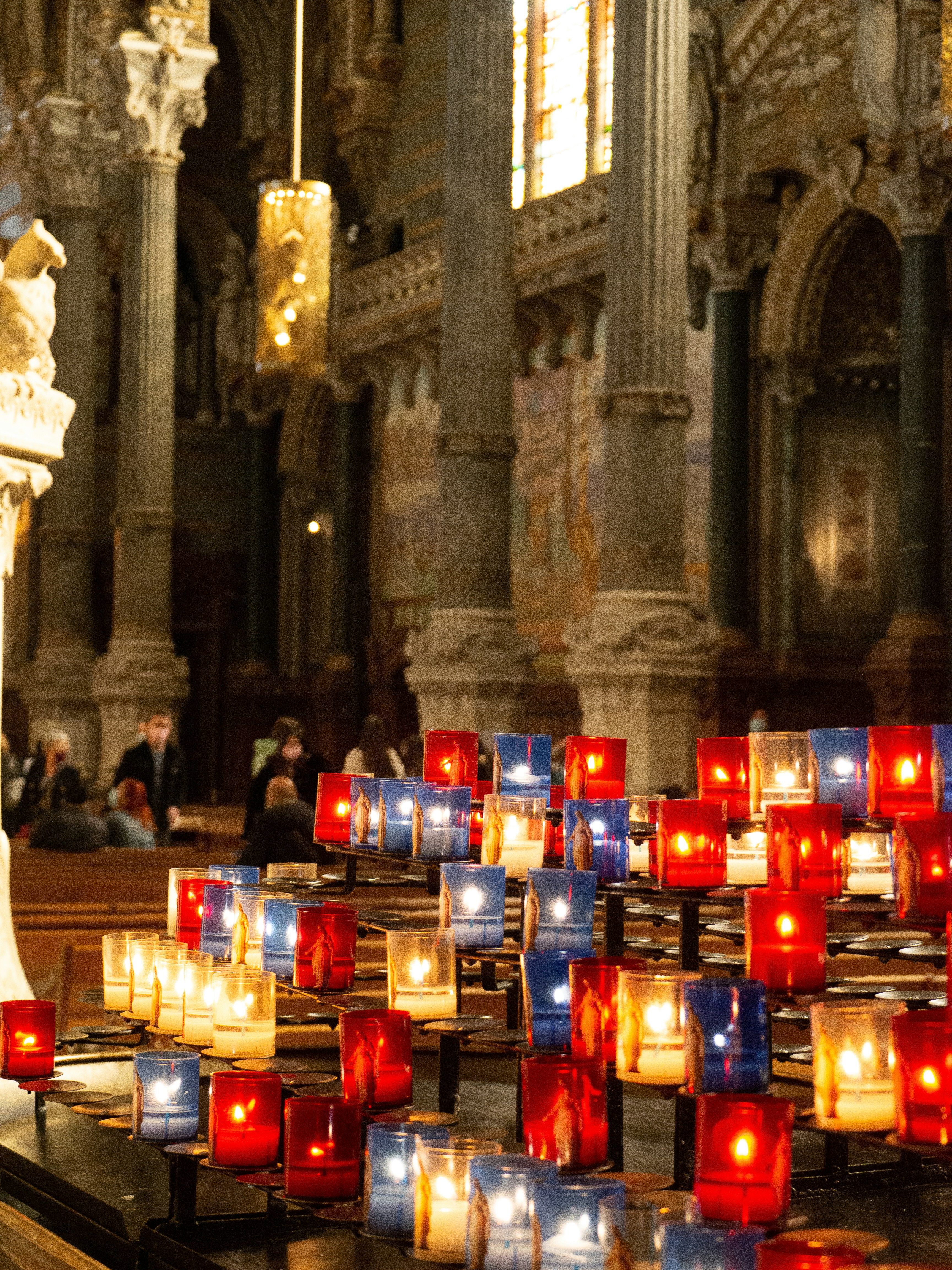 Vibrant candles in red, blue, and white illuminate a serene interior, highlighting the ornate architecture and quiet reverence of the space.