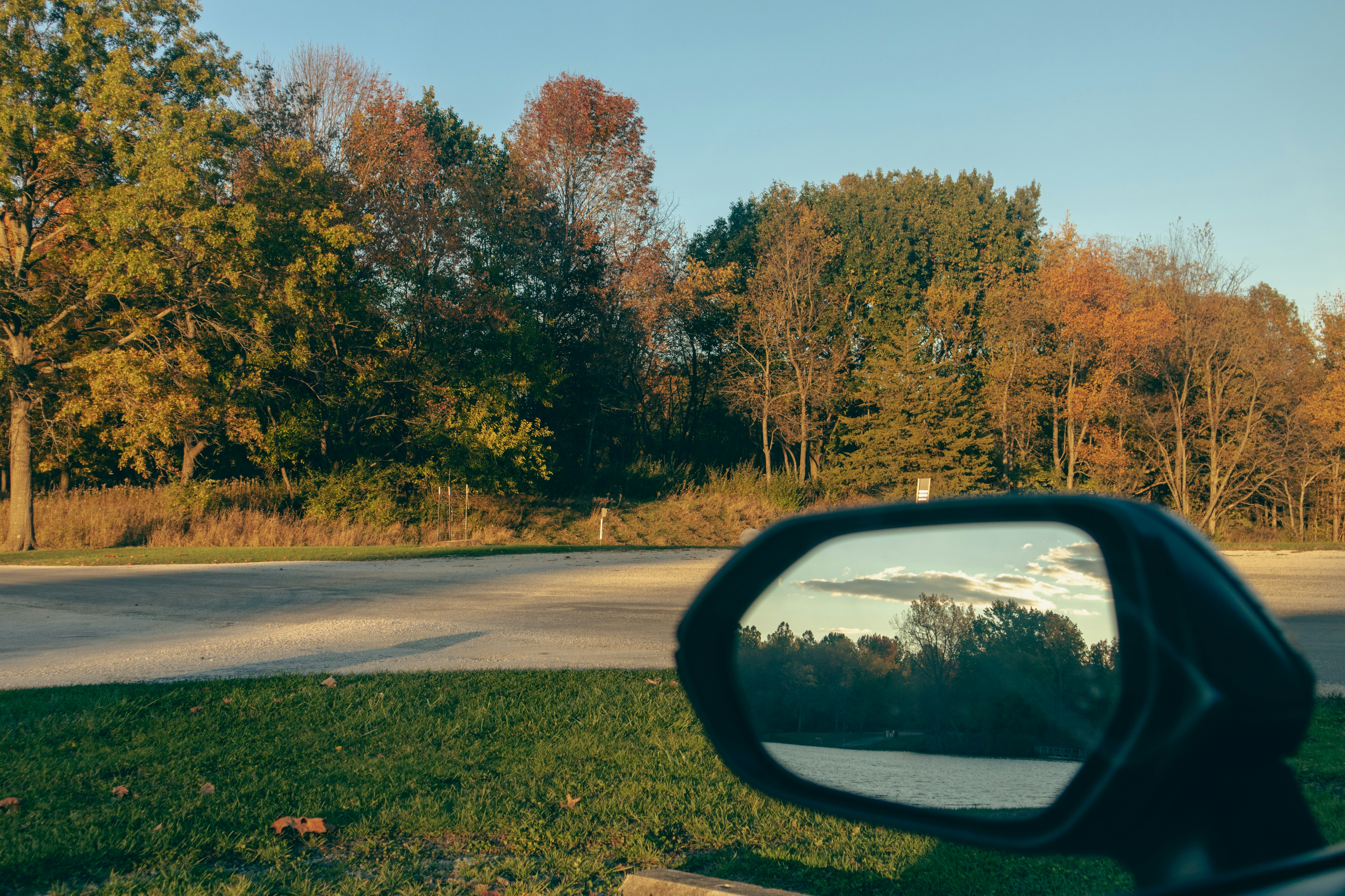 Autumn foliage reflected in a car's side mirror, showcasing vibrant colors and a serene landscape. The scene captures the essence of a peaceful drive in the fall.