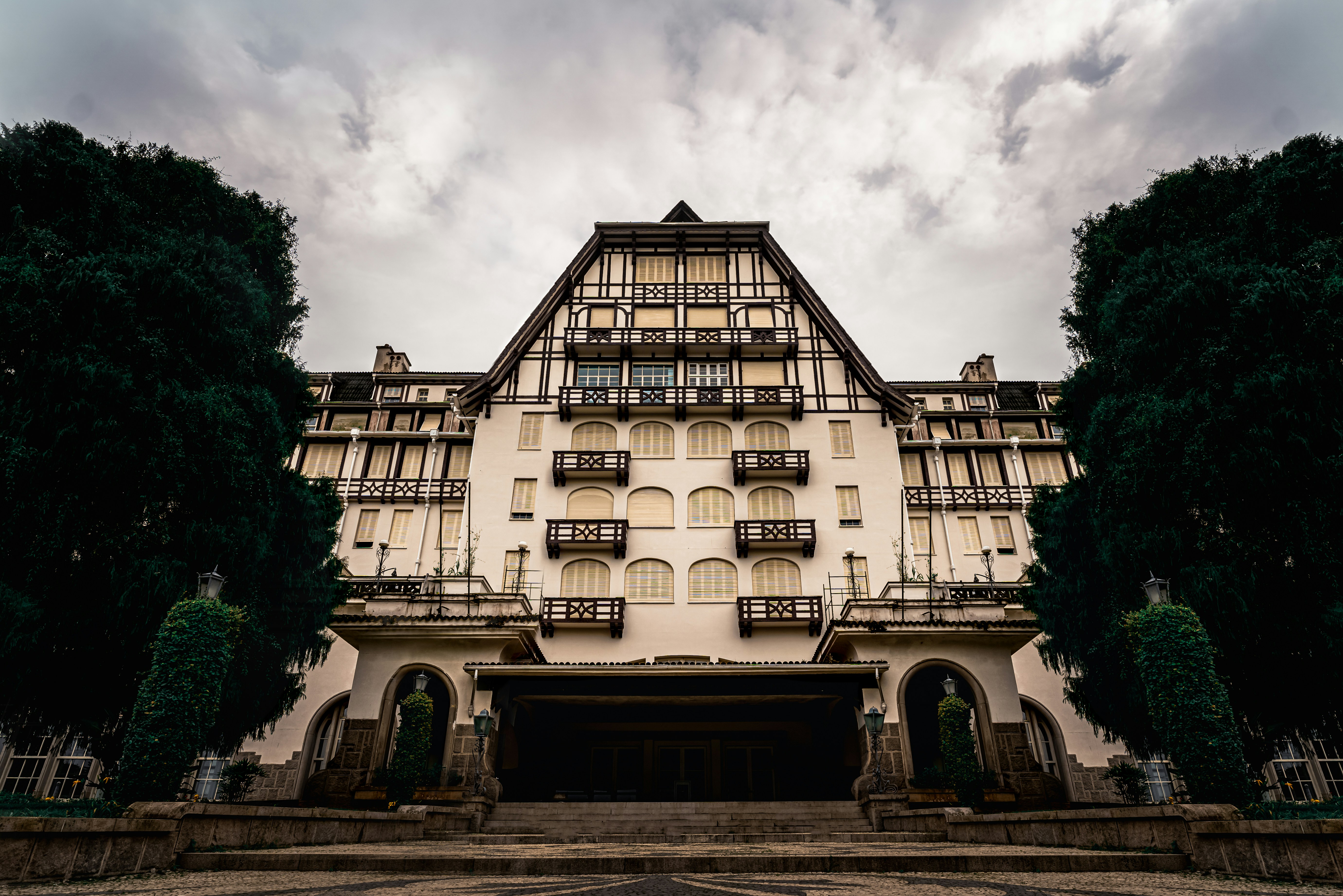 Historic building with symmetrical design framed by dark trees under a dramatic cloudy sky.