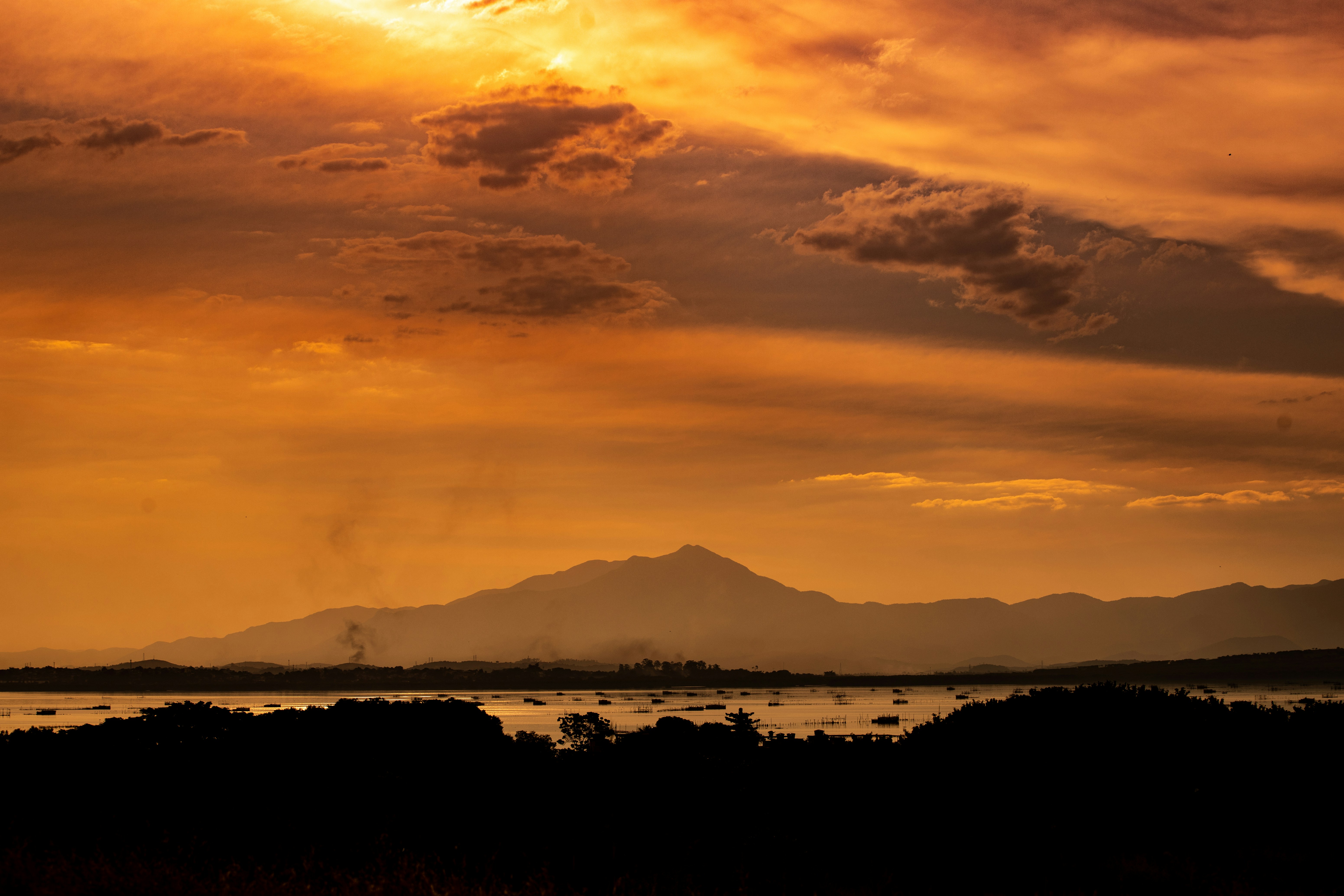 Sunset casting warm hues over a calm body of water with distant mountain silhouettes.