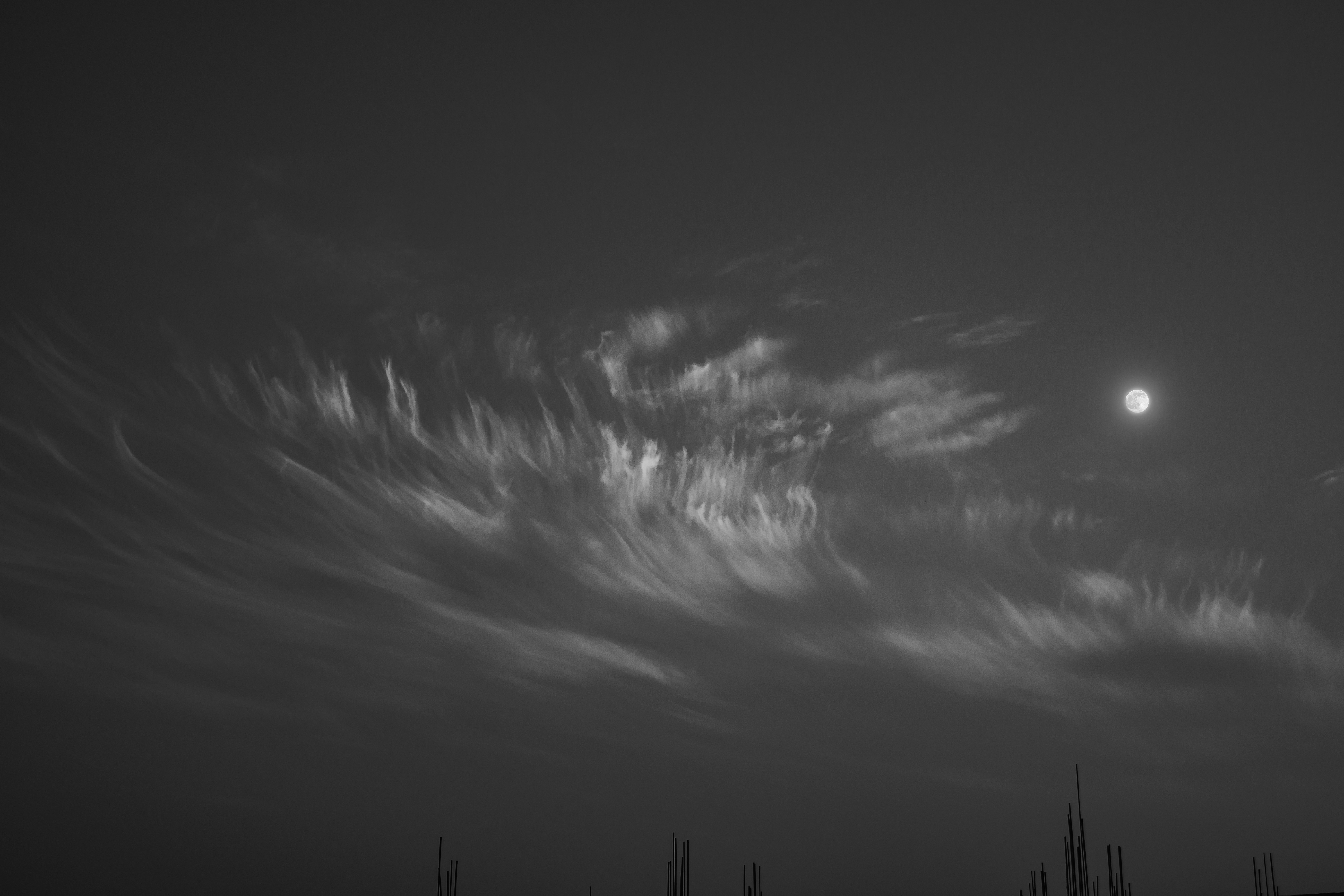 Soft, swirling clouds dance across a twilight sky, illuminated by a glowing moon. The scene conveys a serene and atmospheric moment.