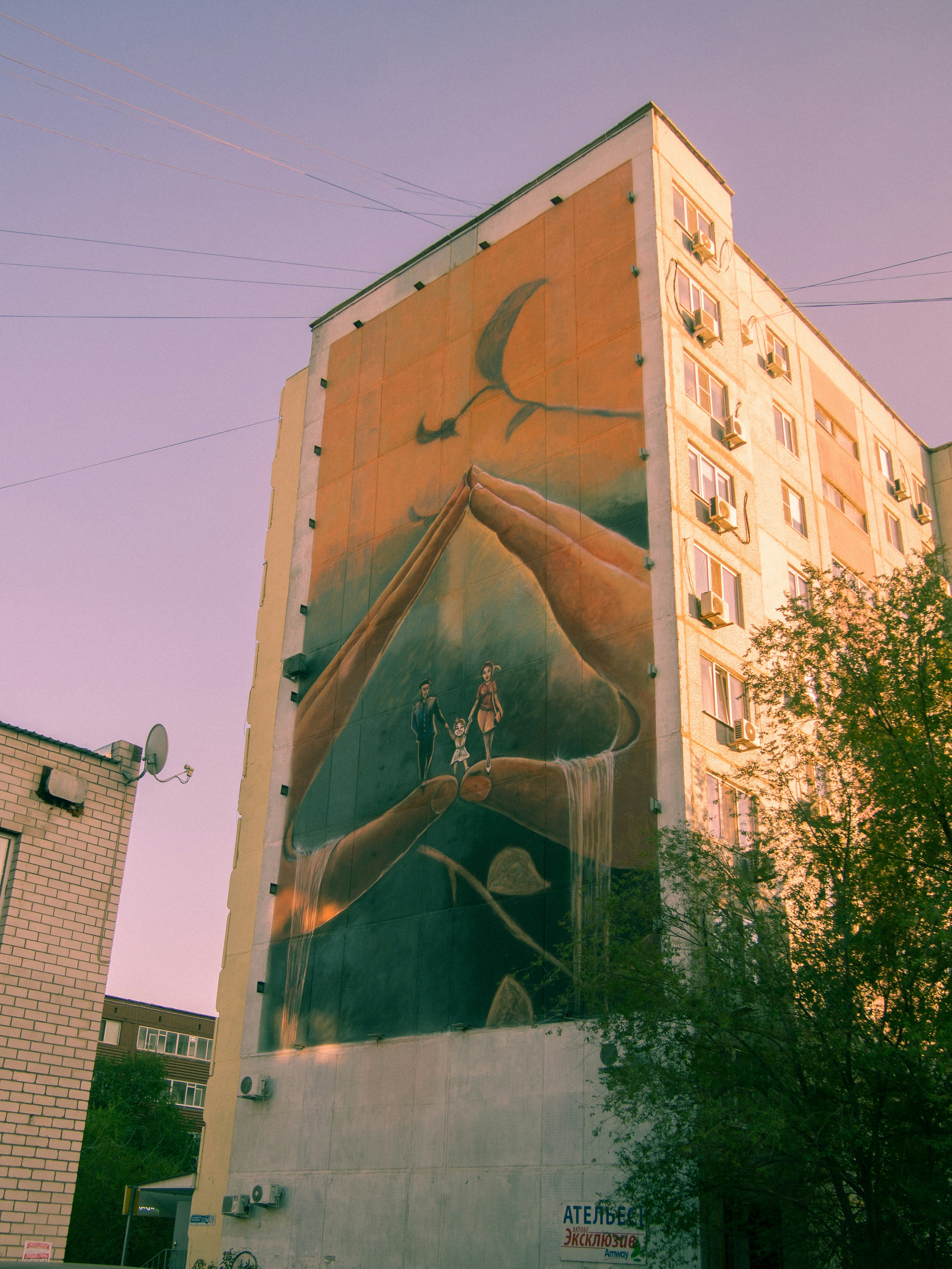 Sunlit mural painting on a high-rise shows hands forming a triangle with two figures, stretching across the building's façade.