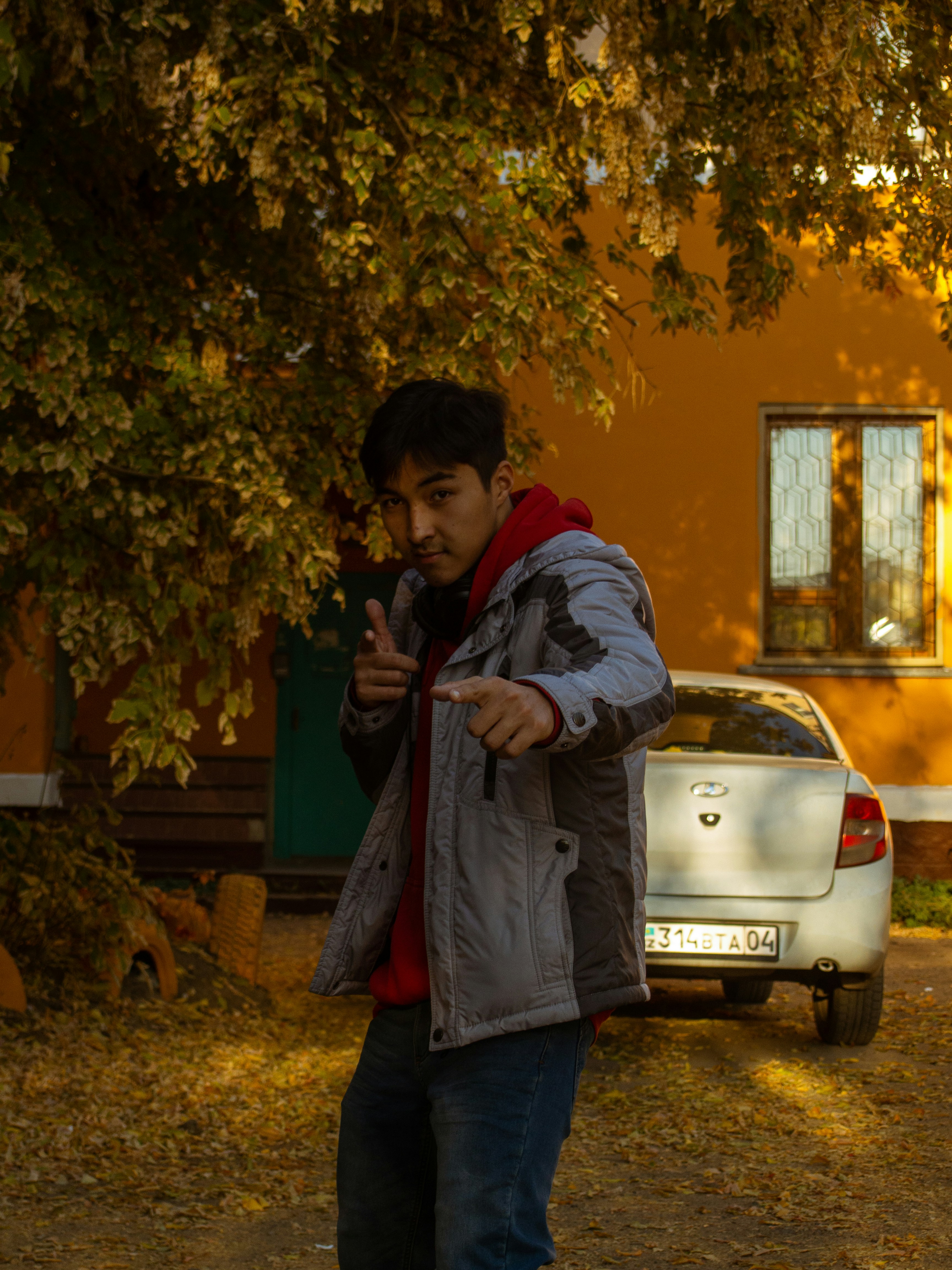 Young man playfully posing in a colorful autumn setting with fallen leaves and a car in the background.