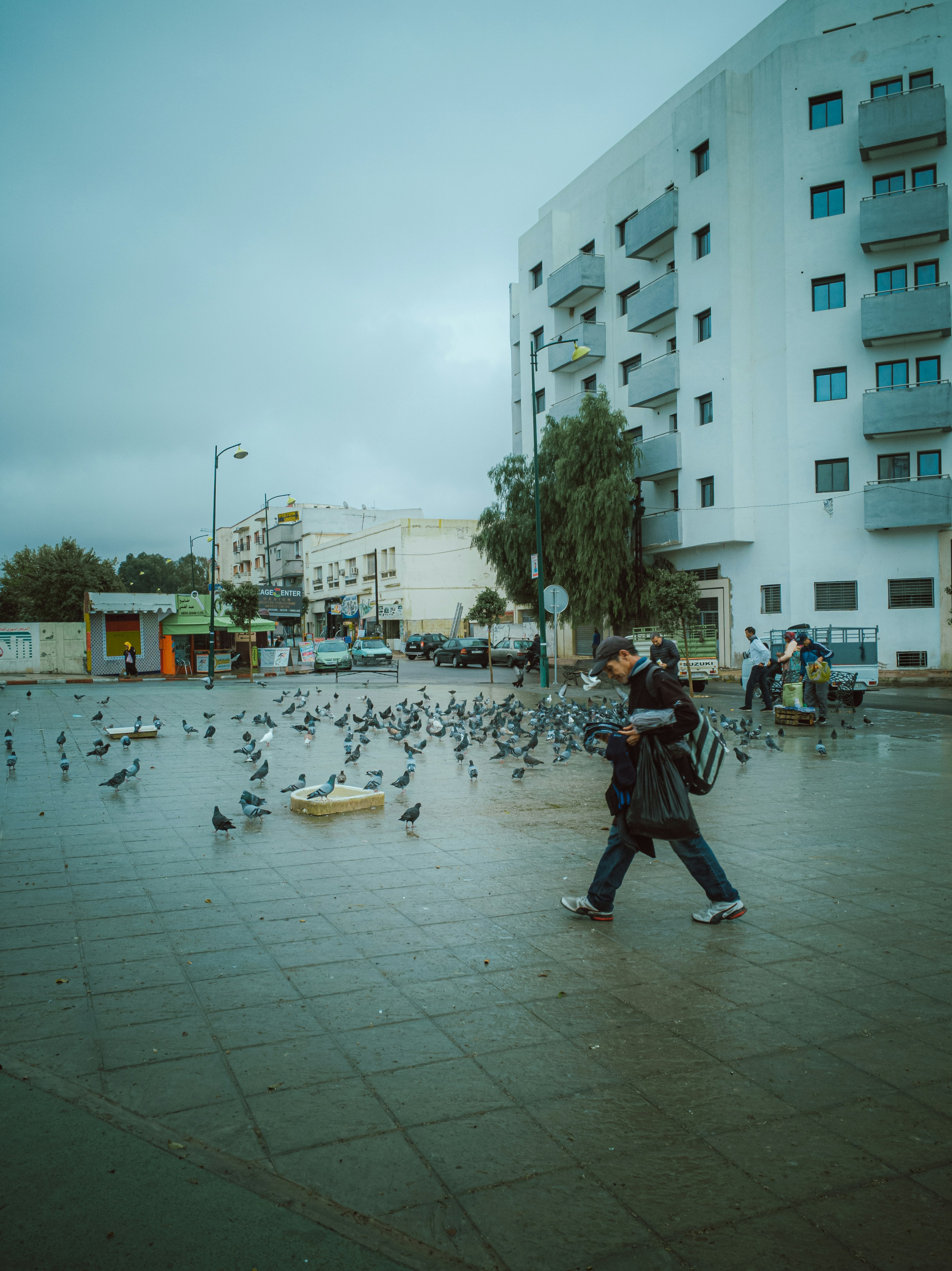 a man walking across a street next to a flock of birds