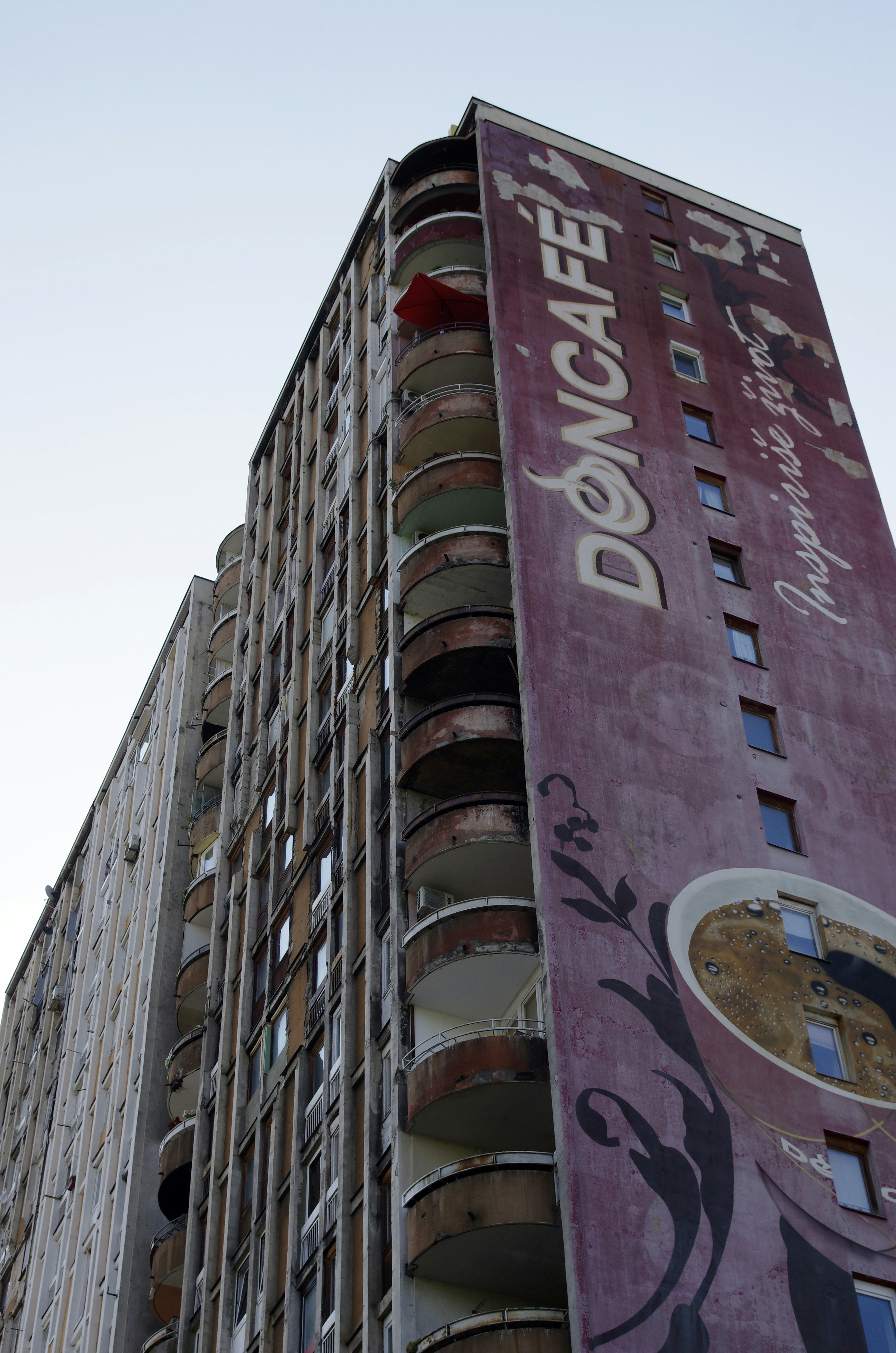 Tide of Purple: A Café Banner Cloaks a Weathered Balcony Tower