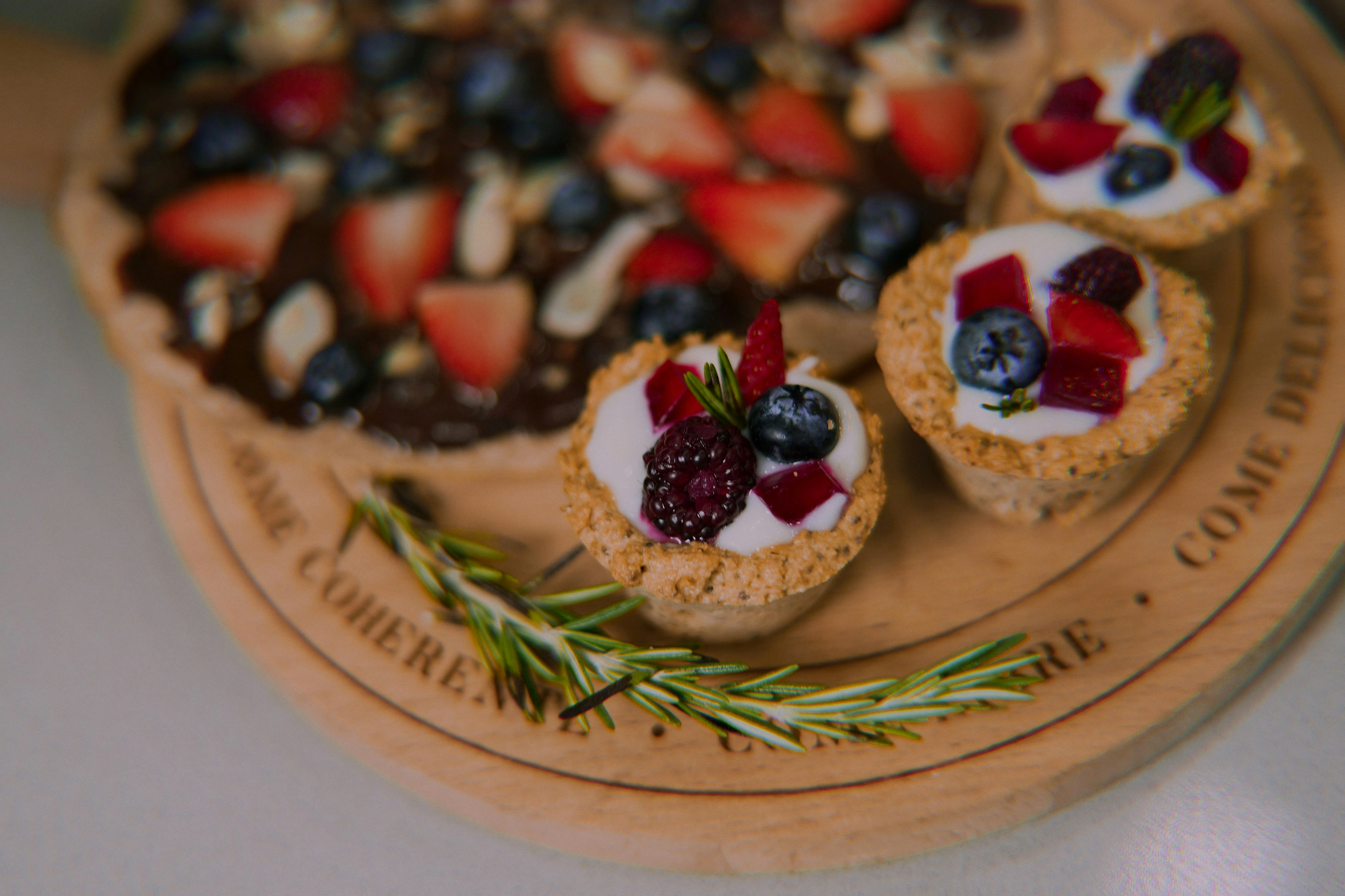 Tarts adorned with fresh berries and a sprig of rosemary on a wooden board.