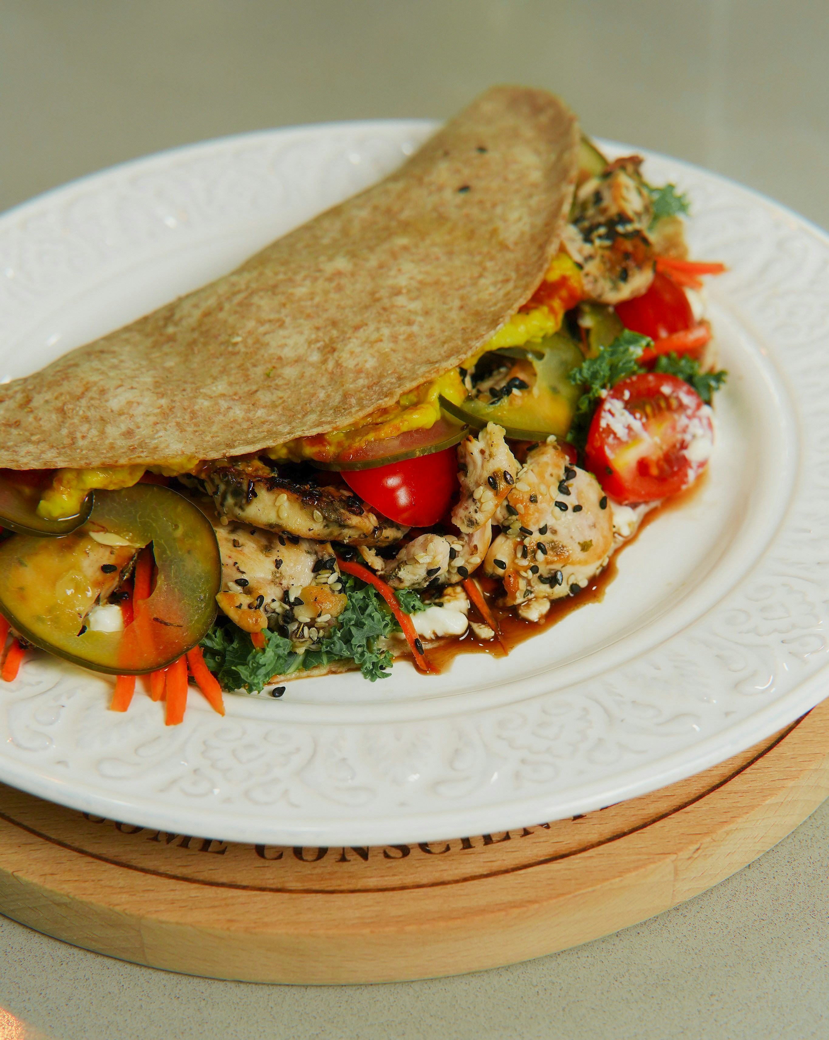 Whole grain taco filled with grilled chicken, cherry tomatoes, pickles, and fresh greens on a white plate.
