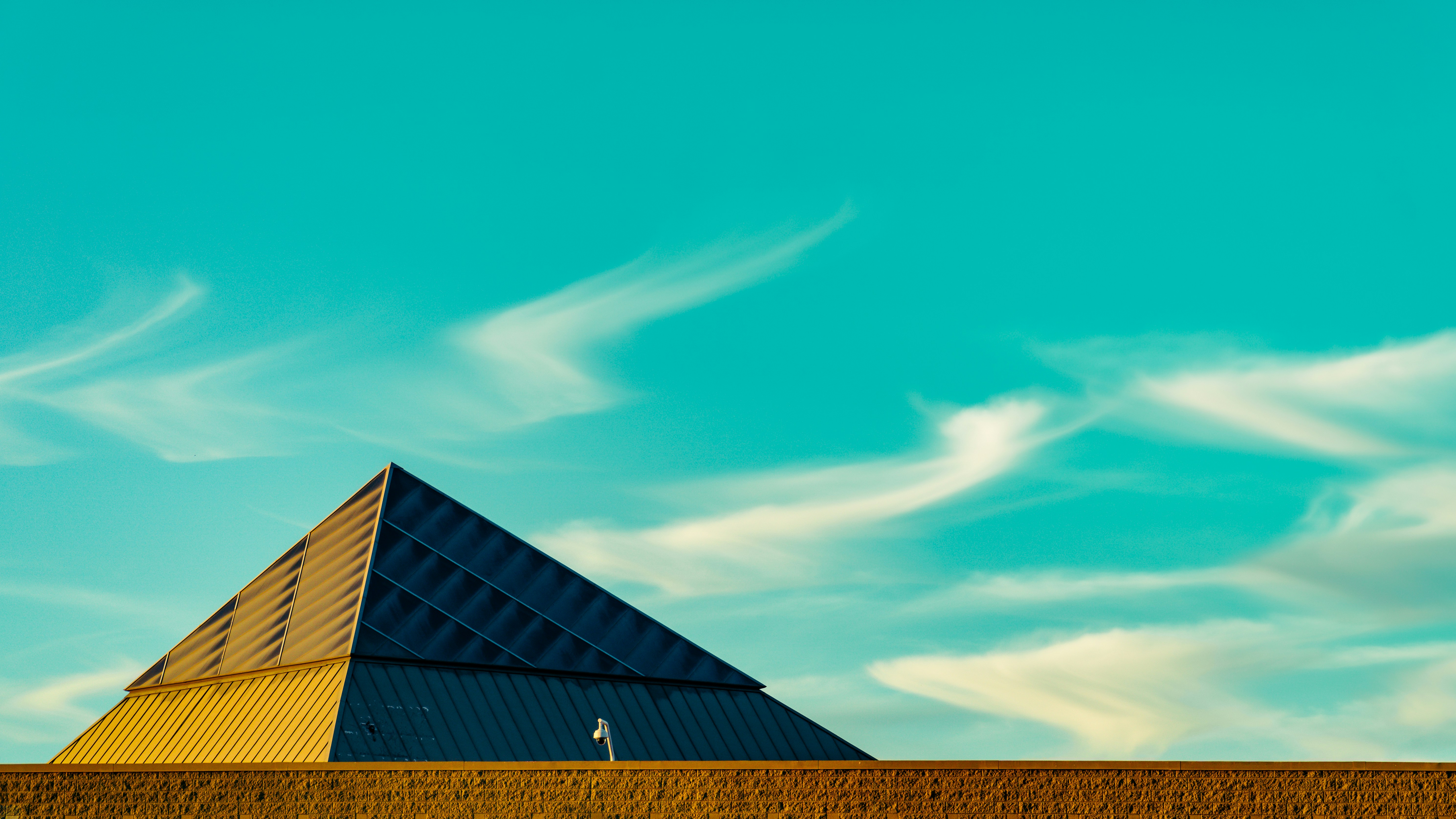 Modern pyramid structure set against a vivid turquoise sky with wispy clouds.