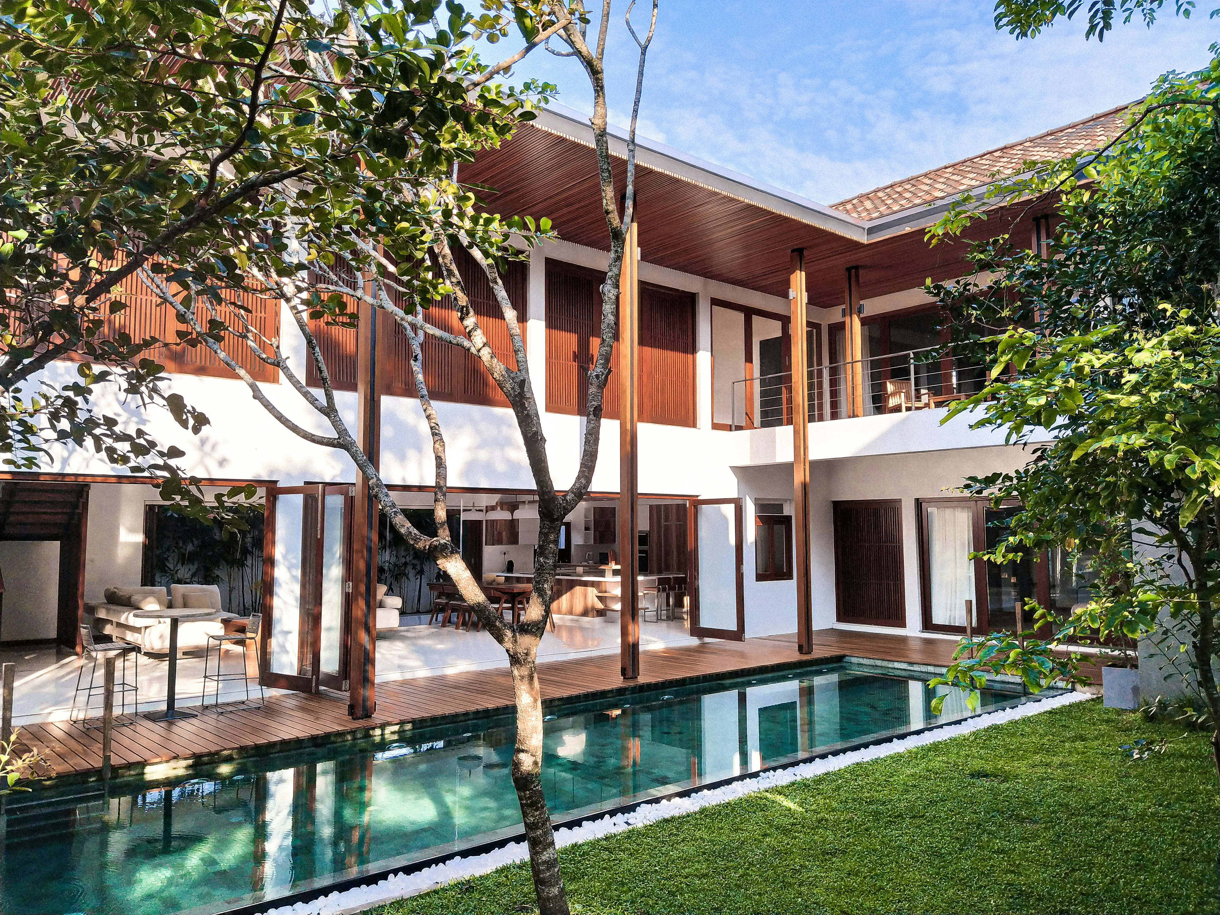 Contemporary house with a sleek pool and lush greenery under a clear blue sky.