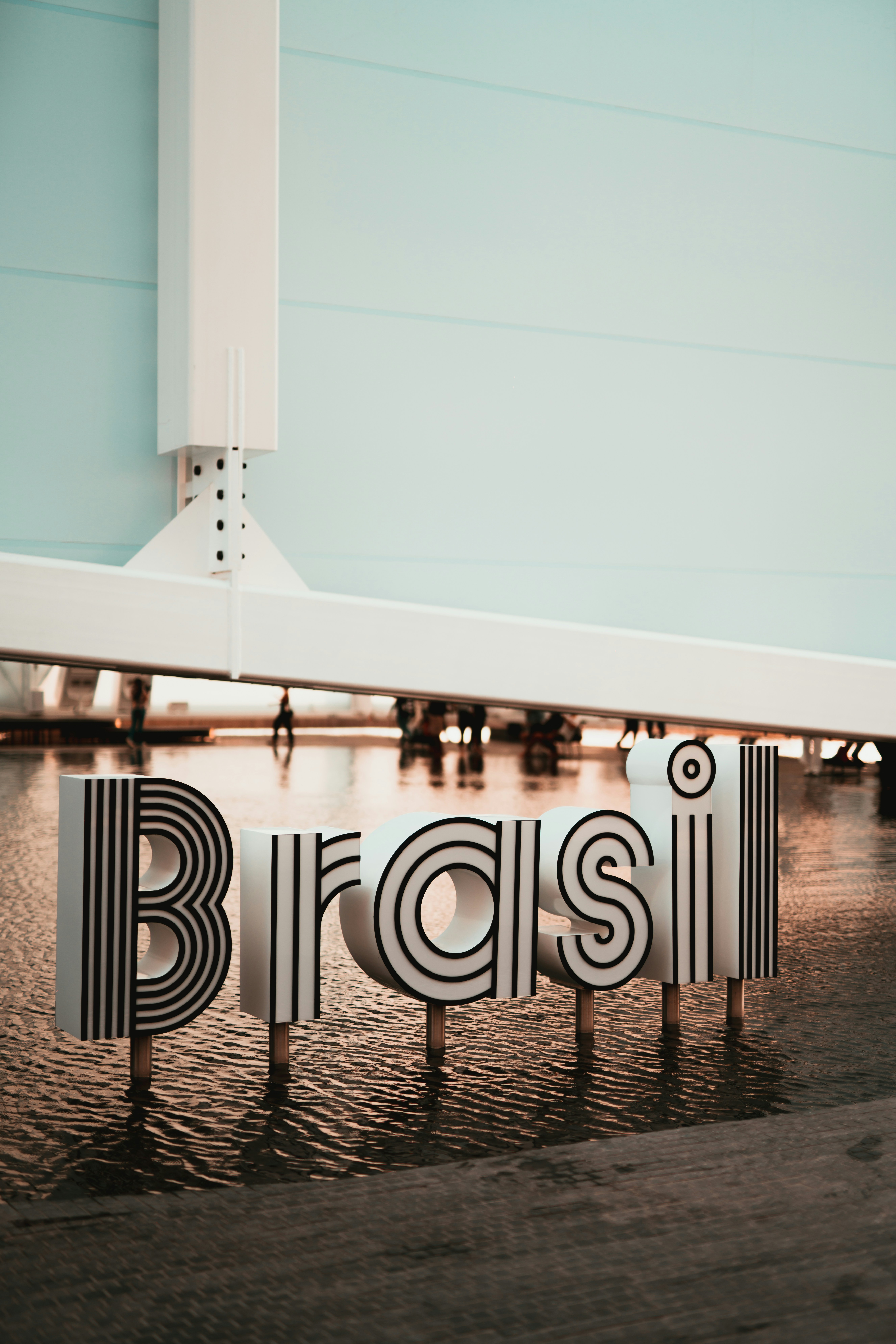 Stylized 'Brasil' sign reflecting on a wet surface, framed by a minimalist architectural backdrop. The design emphasizes modern aesthetics.