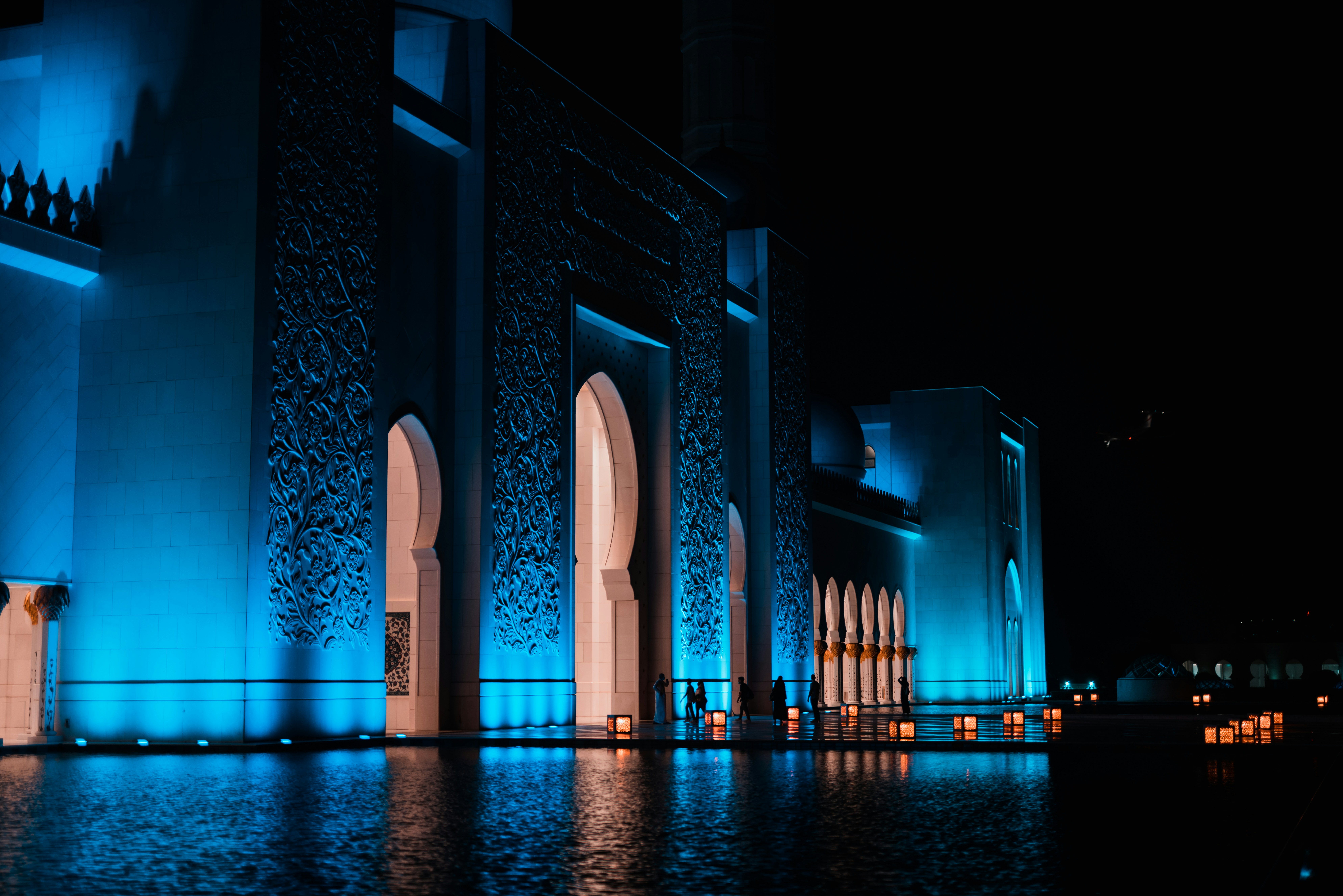 Intricate architectural details illuminated by blue light reflect in the still waters, creating a serene ambiance at night.