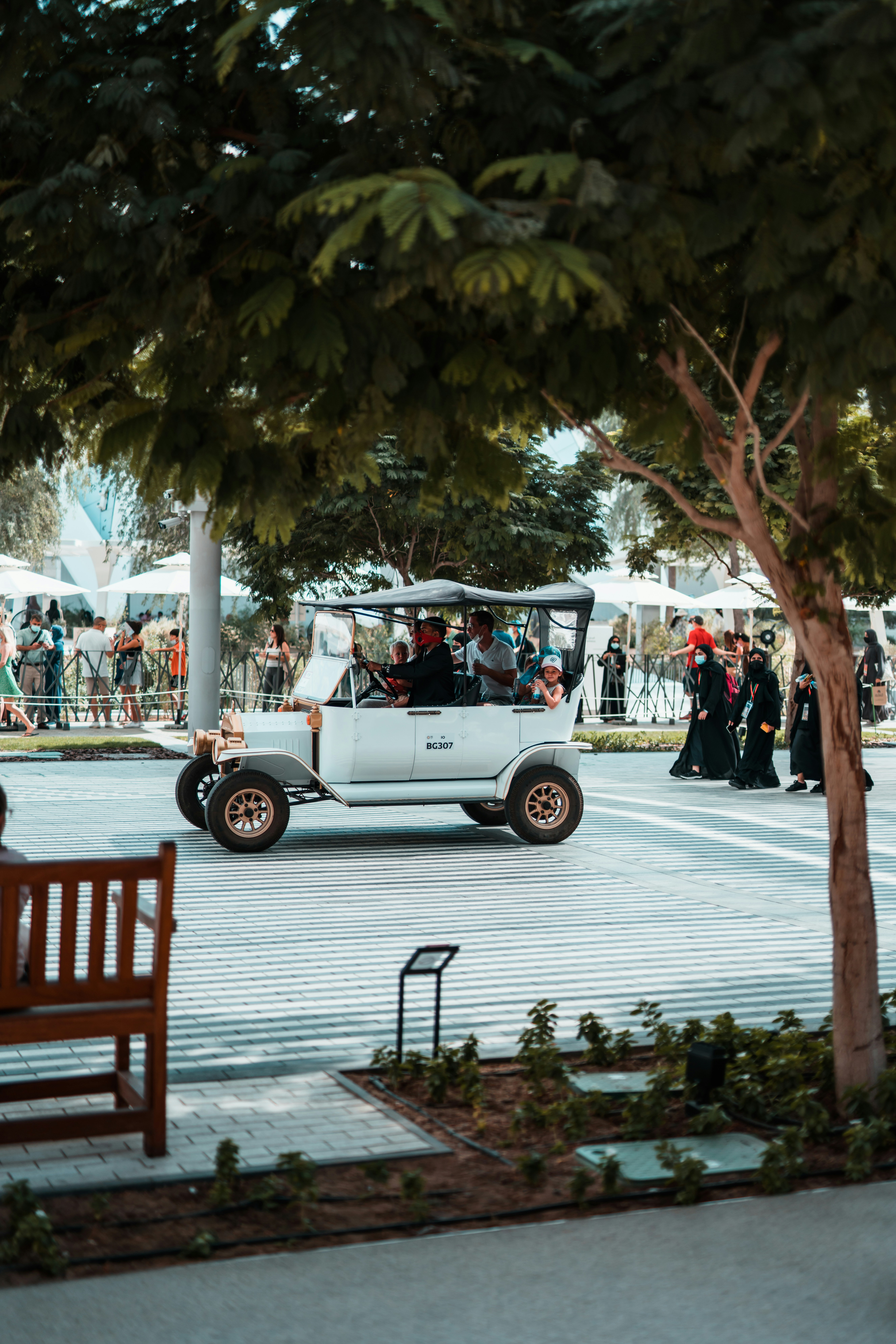 A white car driving down a street next to a park bench photo – Free Car ...