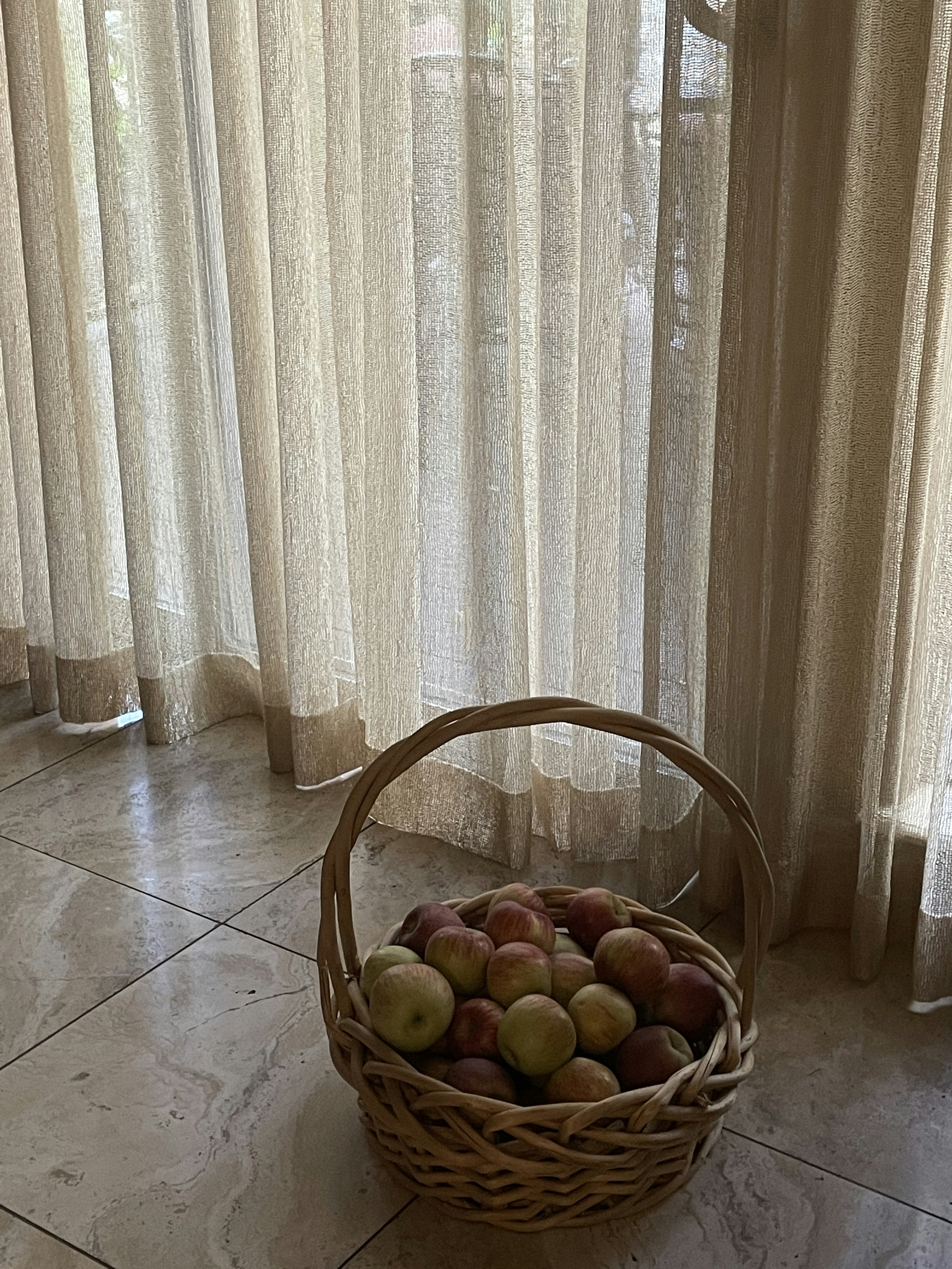 Basket of Apples Beneath Sheer Curtain Light on Marble Floor