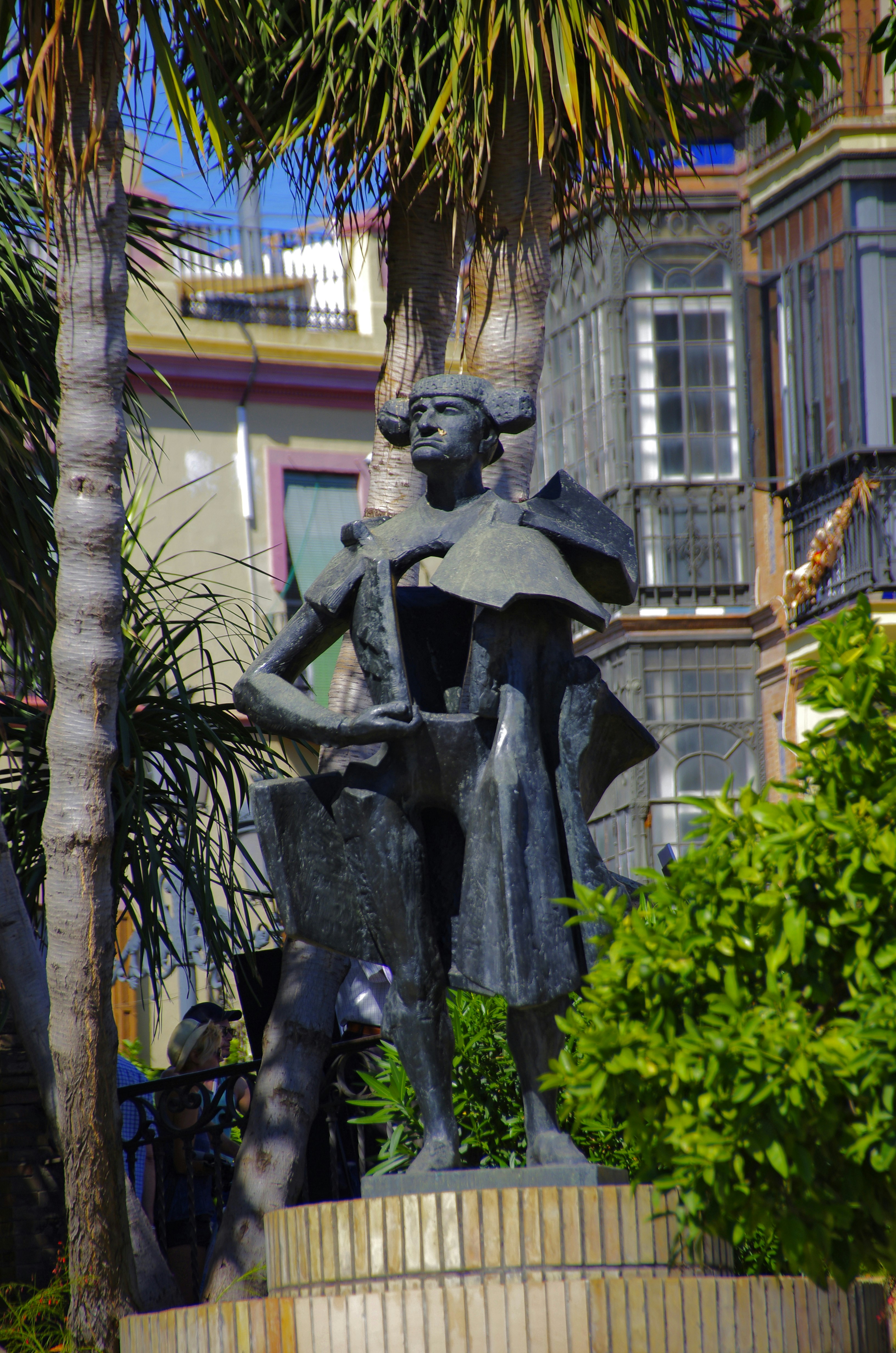 Bronze sculpture of a figure standing amidst lush greenery and urban architecture, symbolizing resilience and artistry.
