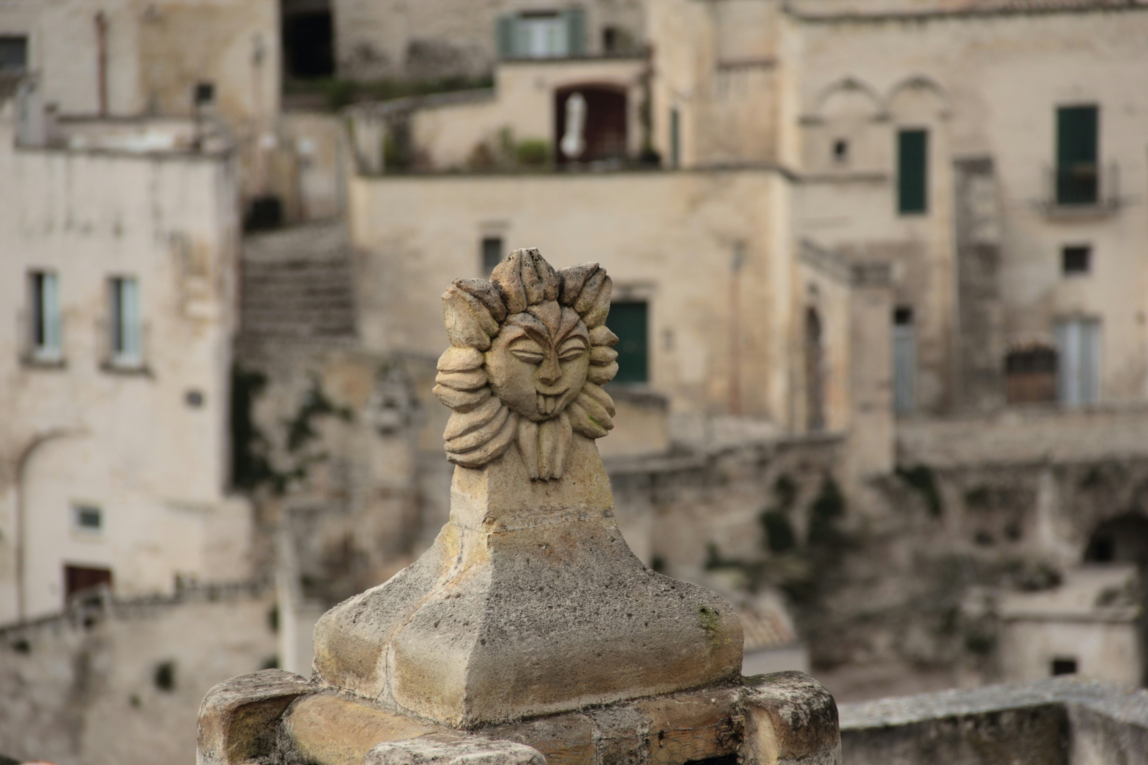 Stone lion statue perched atop a building with a backdrop of aged, rustic architecture.