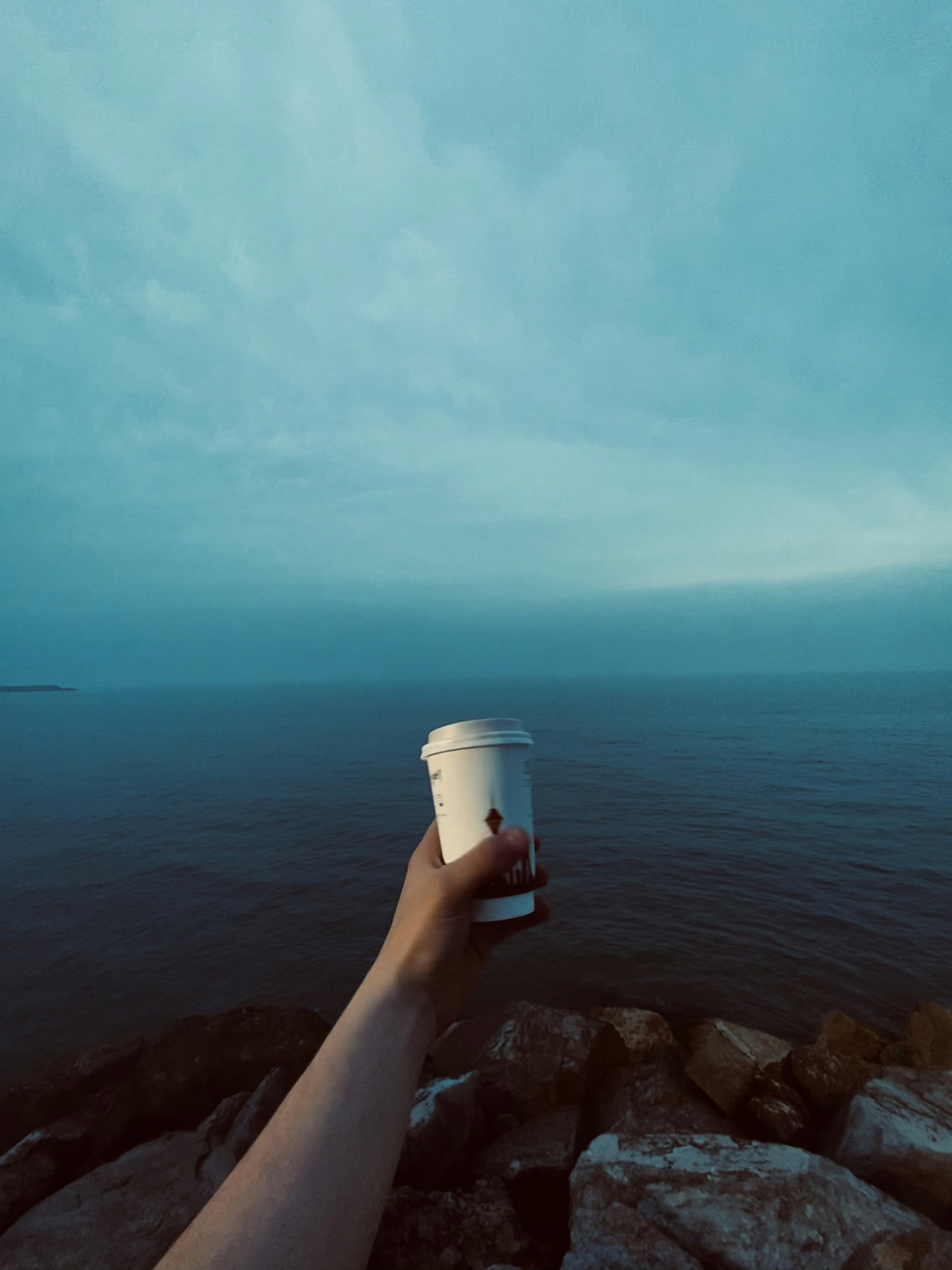 Coastal Latte: Hand Reaches a White Cup Toward the Quiet Ocean Horizon