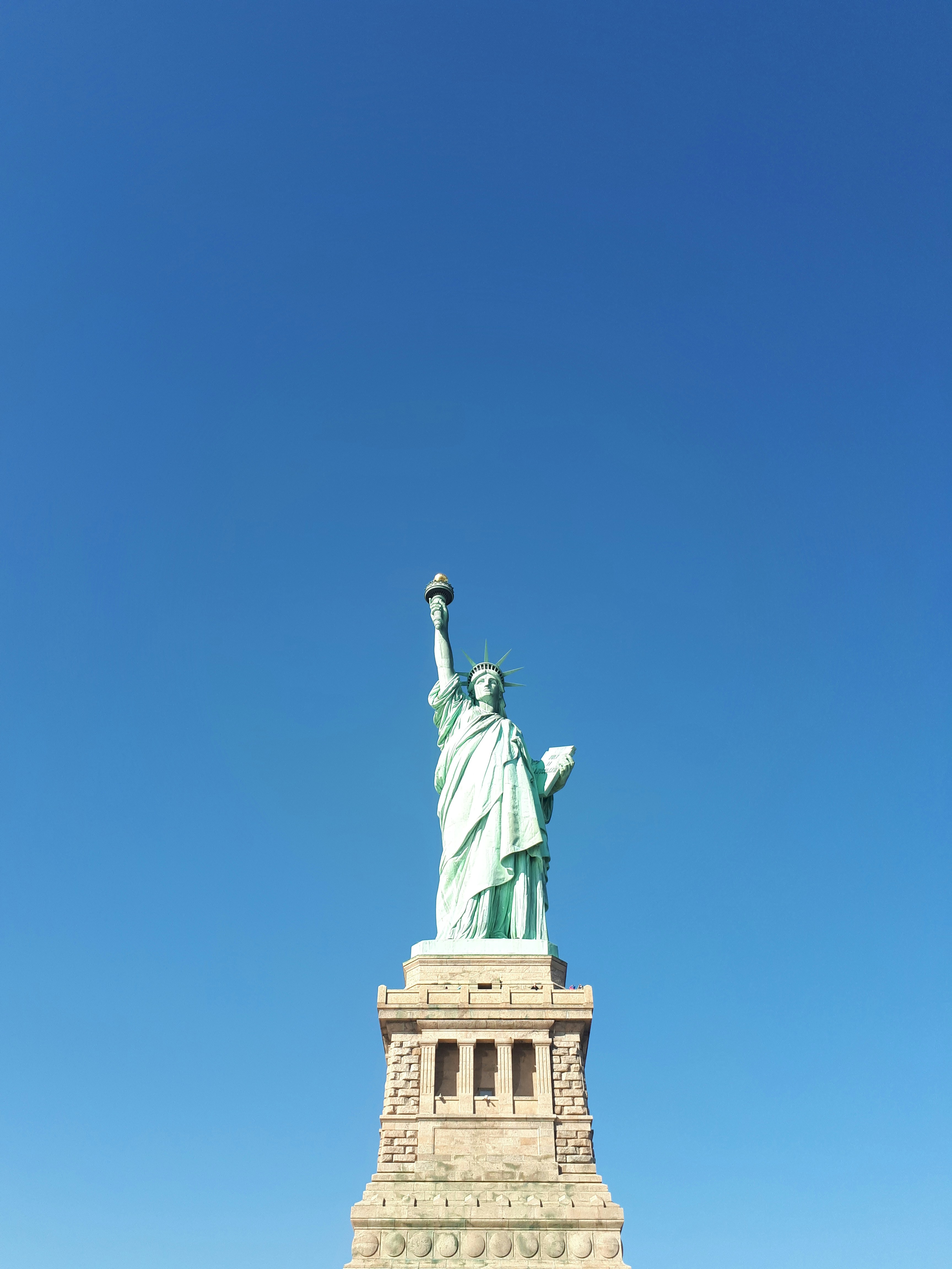 Statue of Liberty standing tall with torch raised, set against a vibrant blue sky.