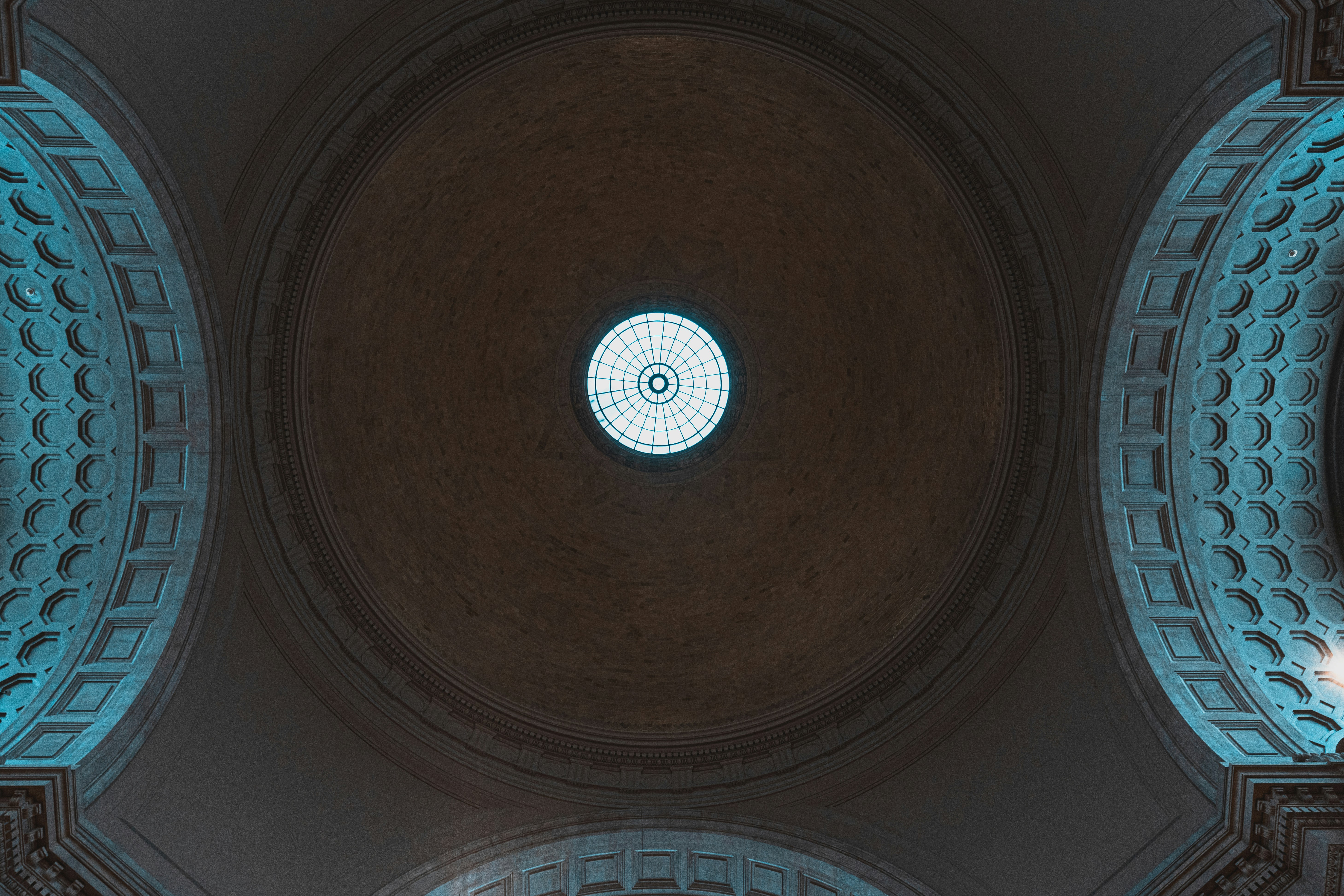 Intricate dome ceiling featuring a central skylight surrounded by ornate detailing and soft blue lighting.