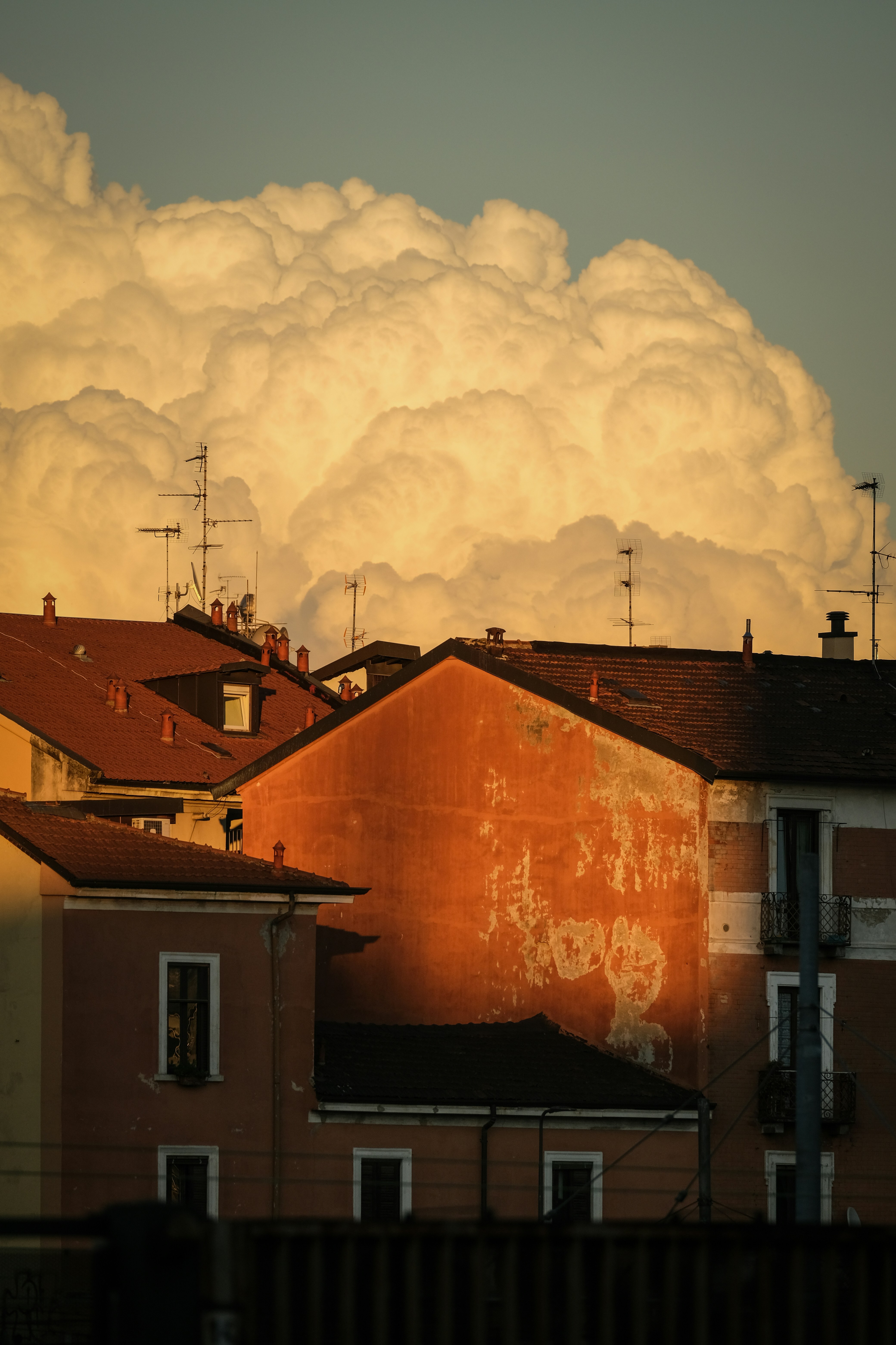 Weathered buildings in an urban setting bask in the warm glow of late afternoon light, contrasting with dramatic cloud formations above.