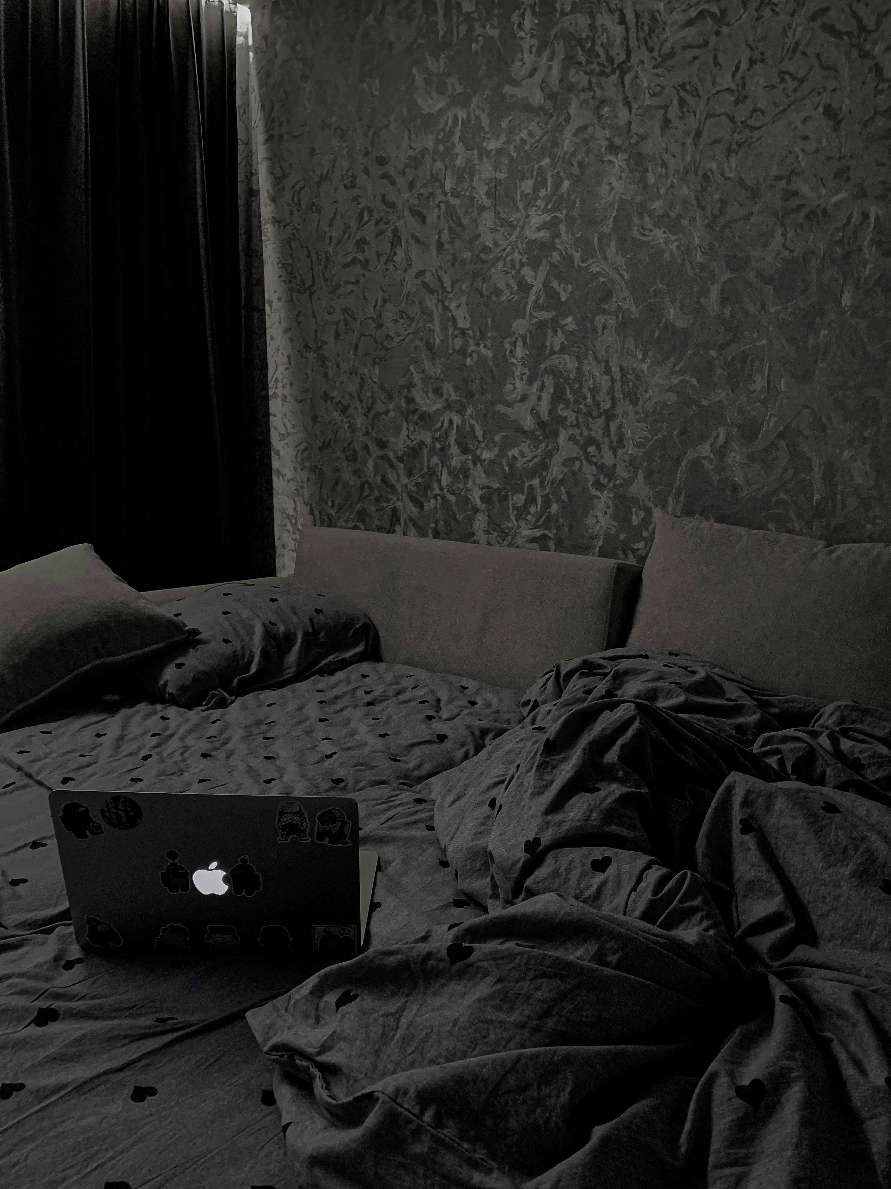 Noir Nook: A Laptop Resting on a Crumpled Bed in Dim Lighting