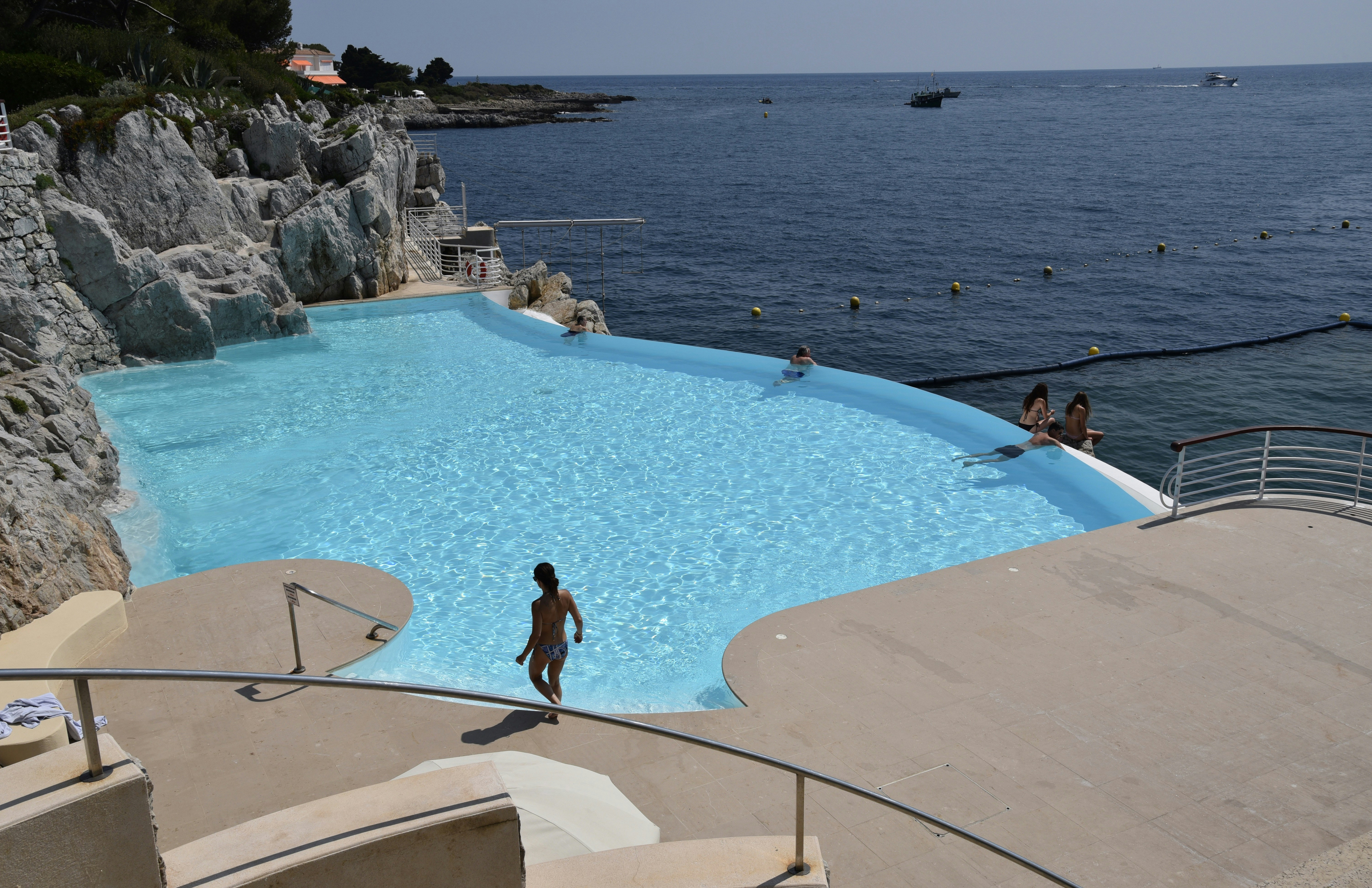 Infinity pool merging with the sea under a clear sky, with swimmers enjoying the tranquil setting.