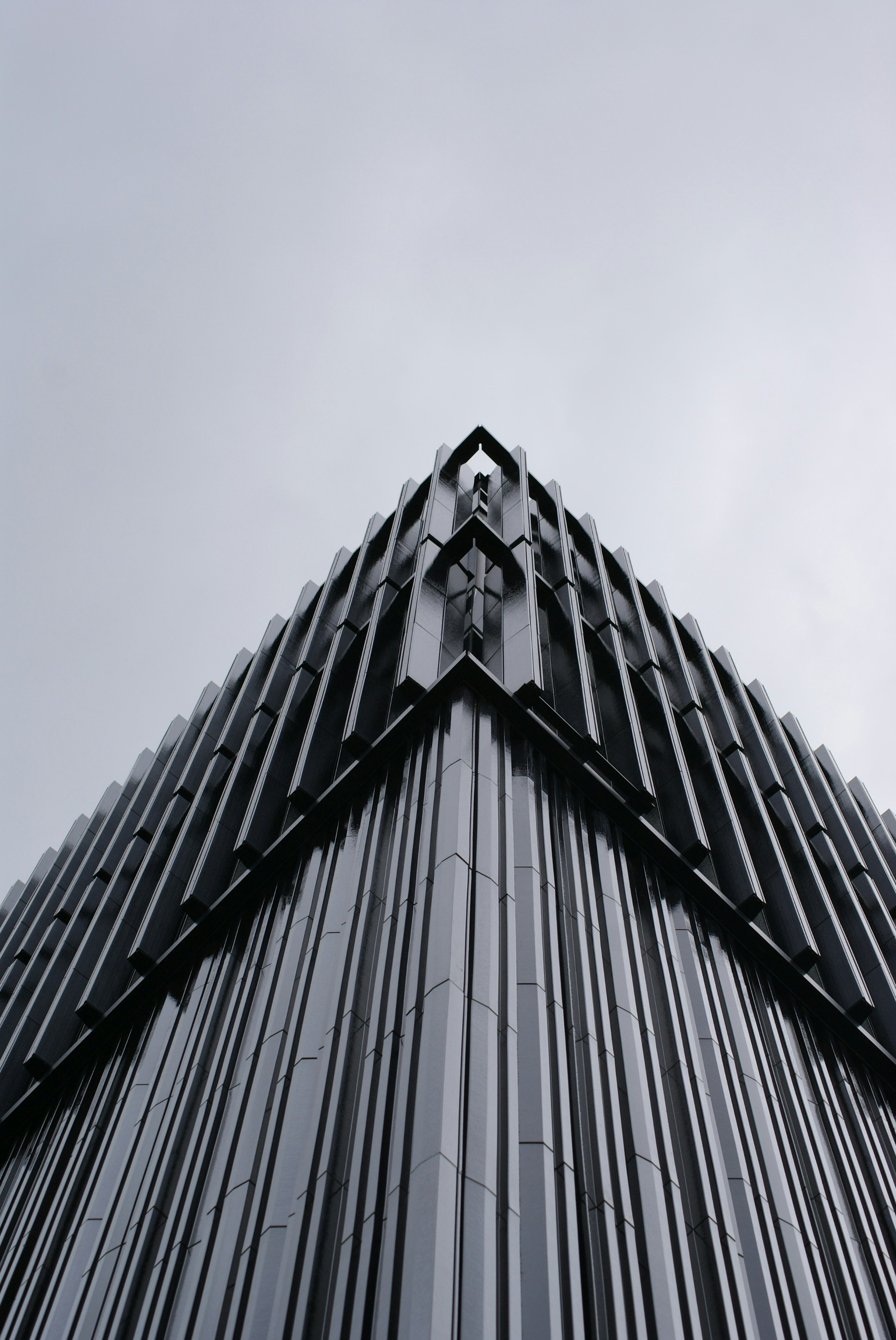 A striking view of a contemporary building's sharp corner, emphasizing its sleek lines and reflective surfaces against a cloudy sky.