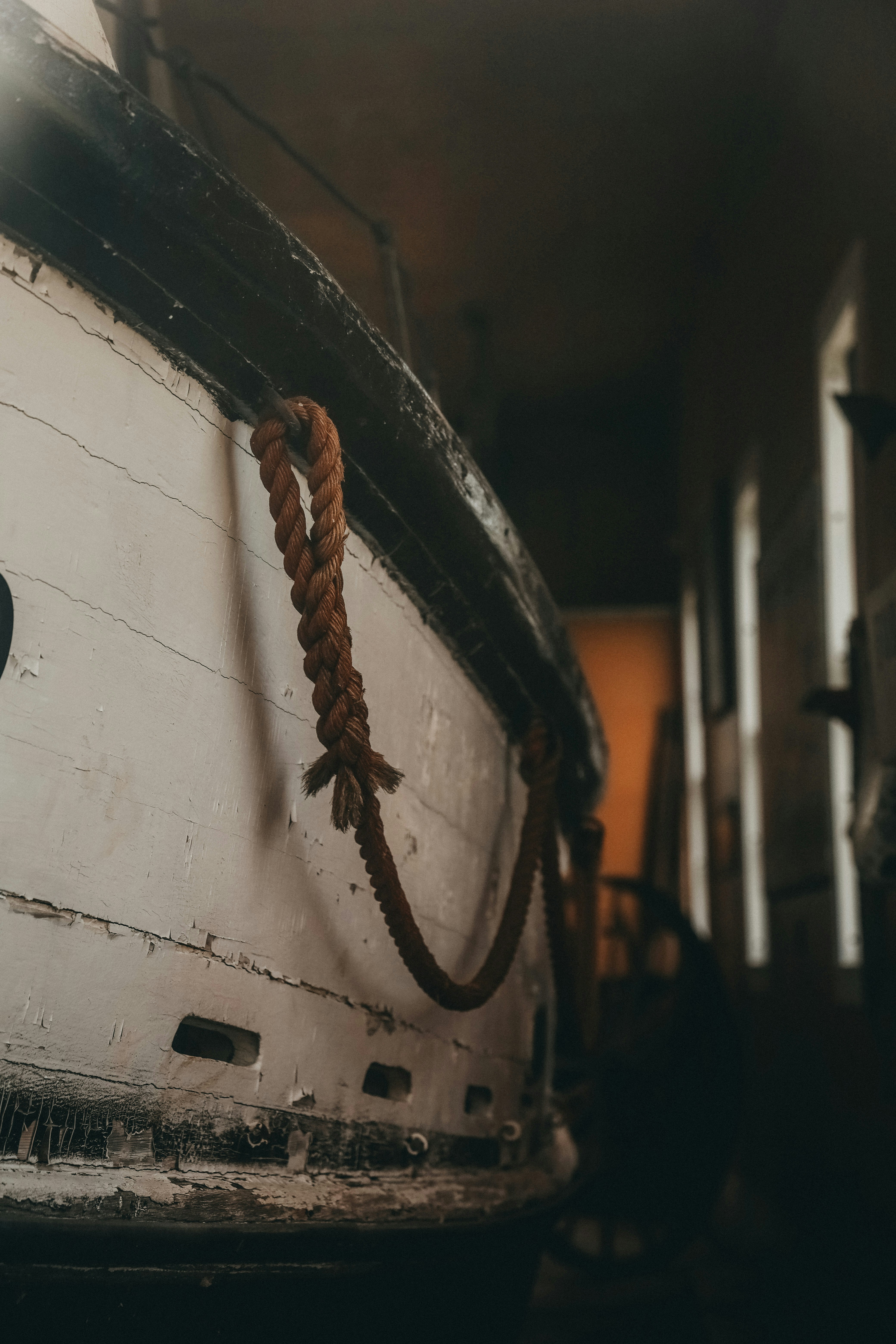 Weathered boat hull adorned with a thick rope, set against a dimly lit interior. The contrast highlights the vessel's storied past.