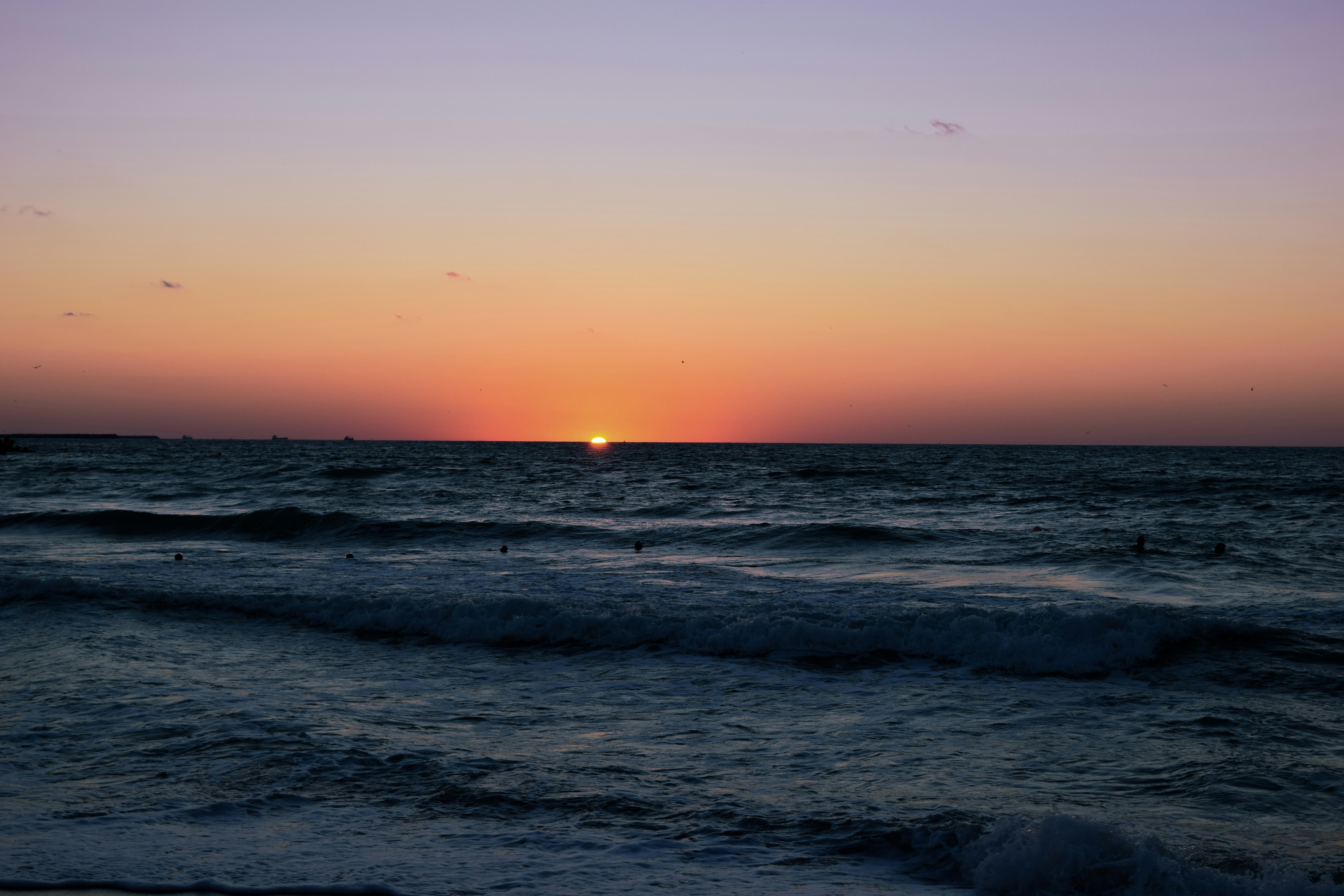 Vibrant sunset casts warm hues over rolling ocean waves, highlighting the tranquil evening atmosphere.