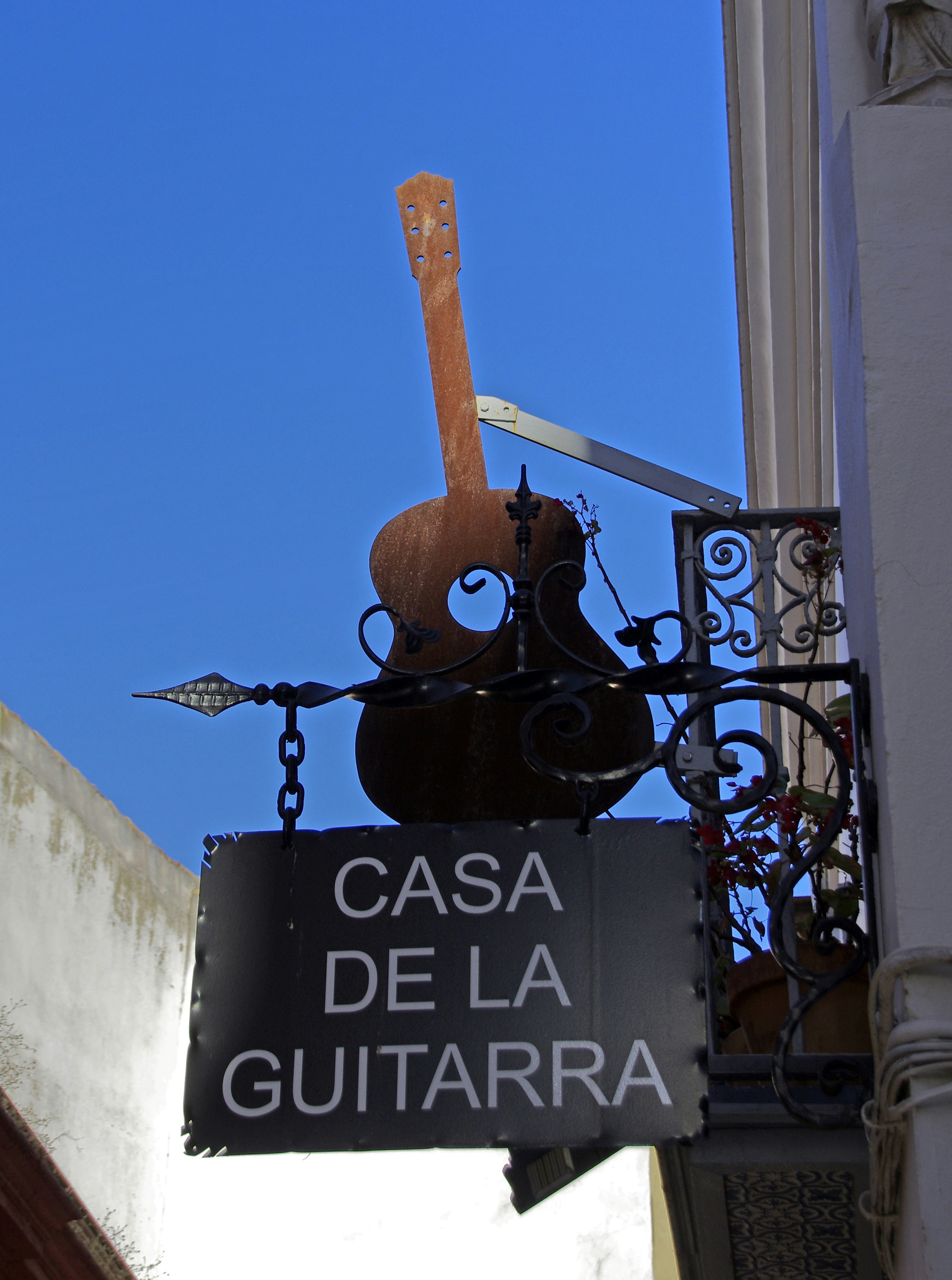 Rusted Guitar Silhouette Guarding the Casa de la Guitarra Sign Against a Crisp Blue Sky