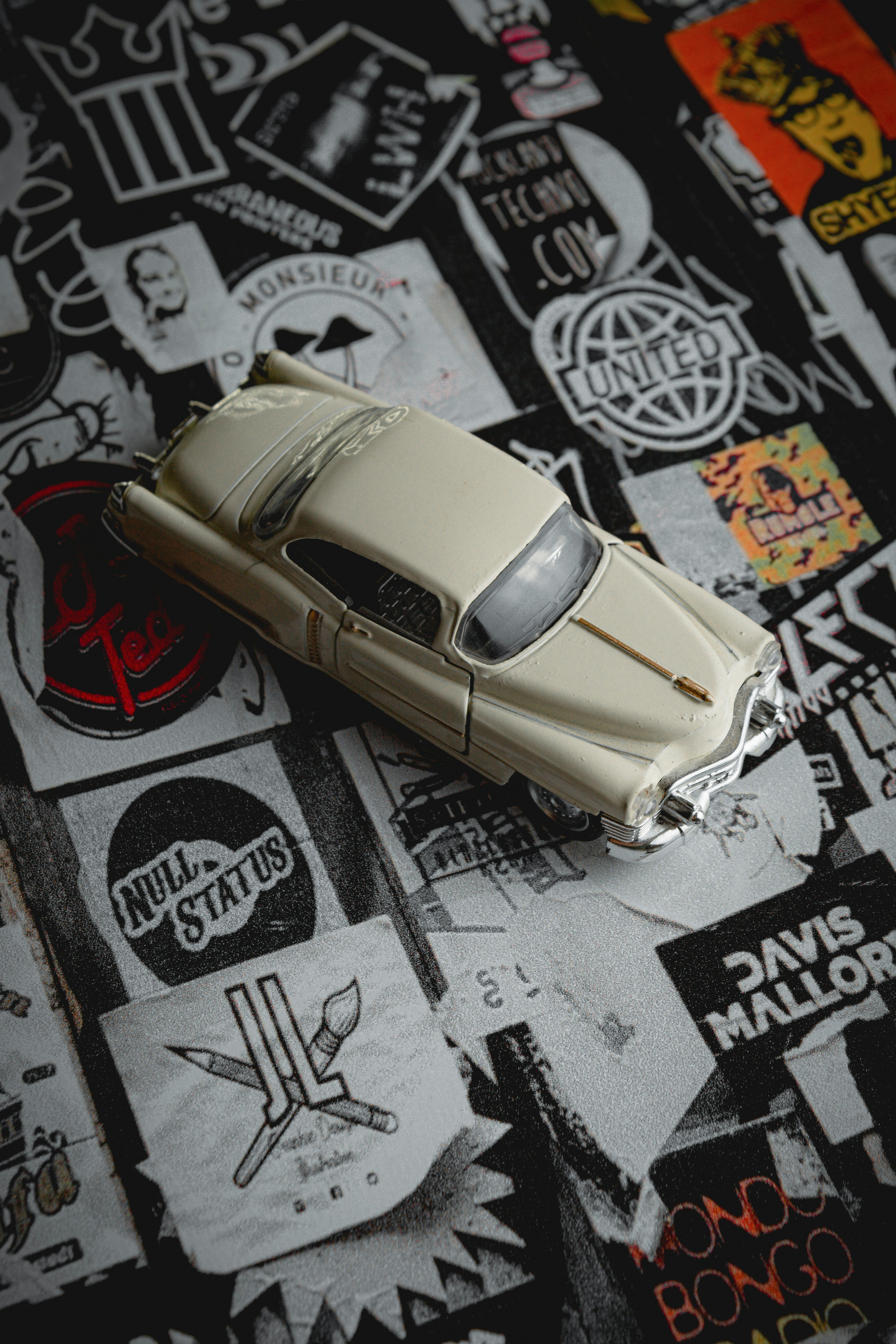 Cream-colored vintage die-cast car atop a sticker-strewn floor