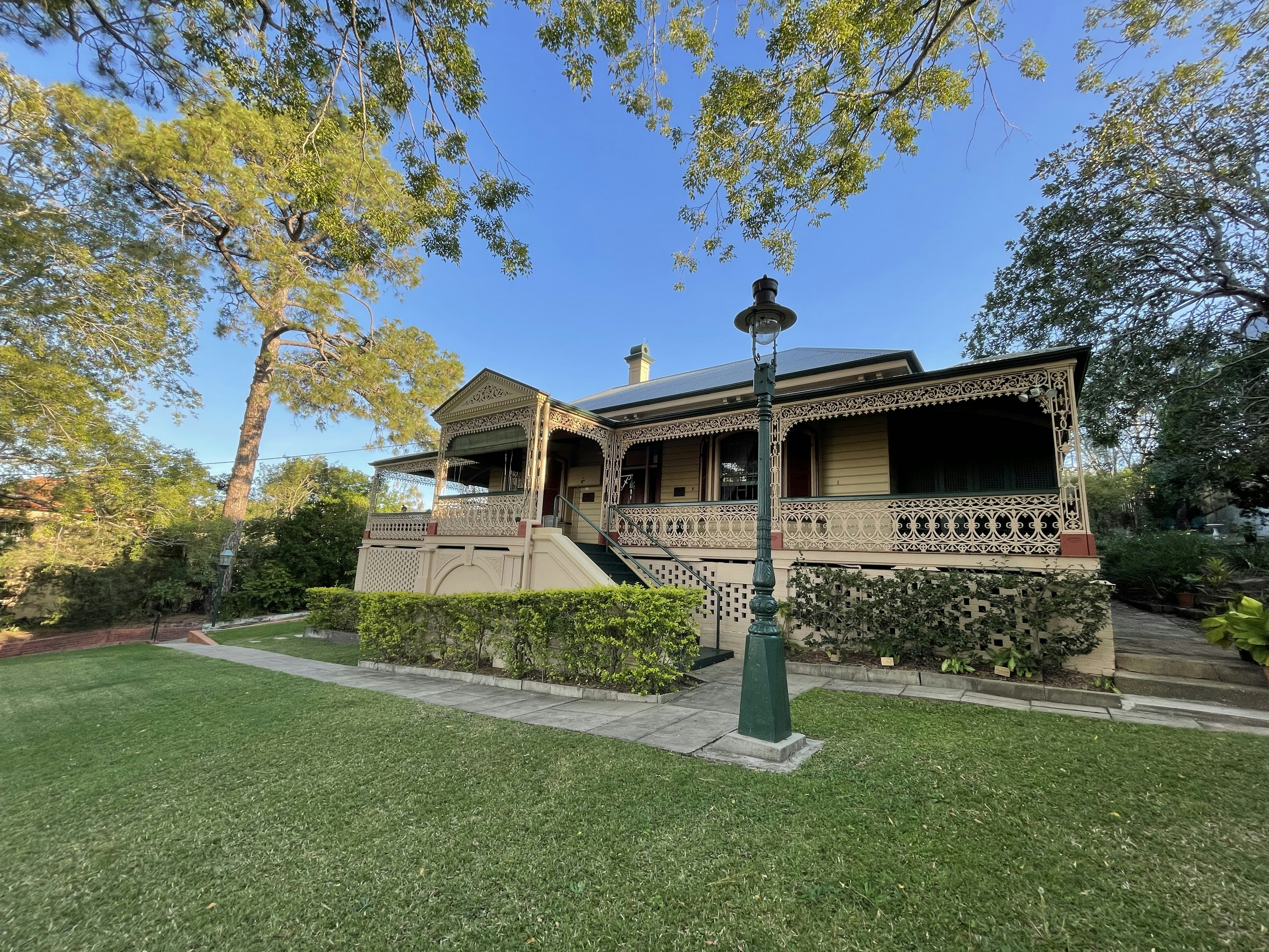 Historic house with intricate Victorian woodwork surrounded by lush greenery under a clear blue sky.