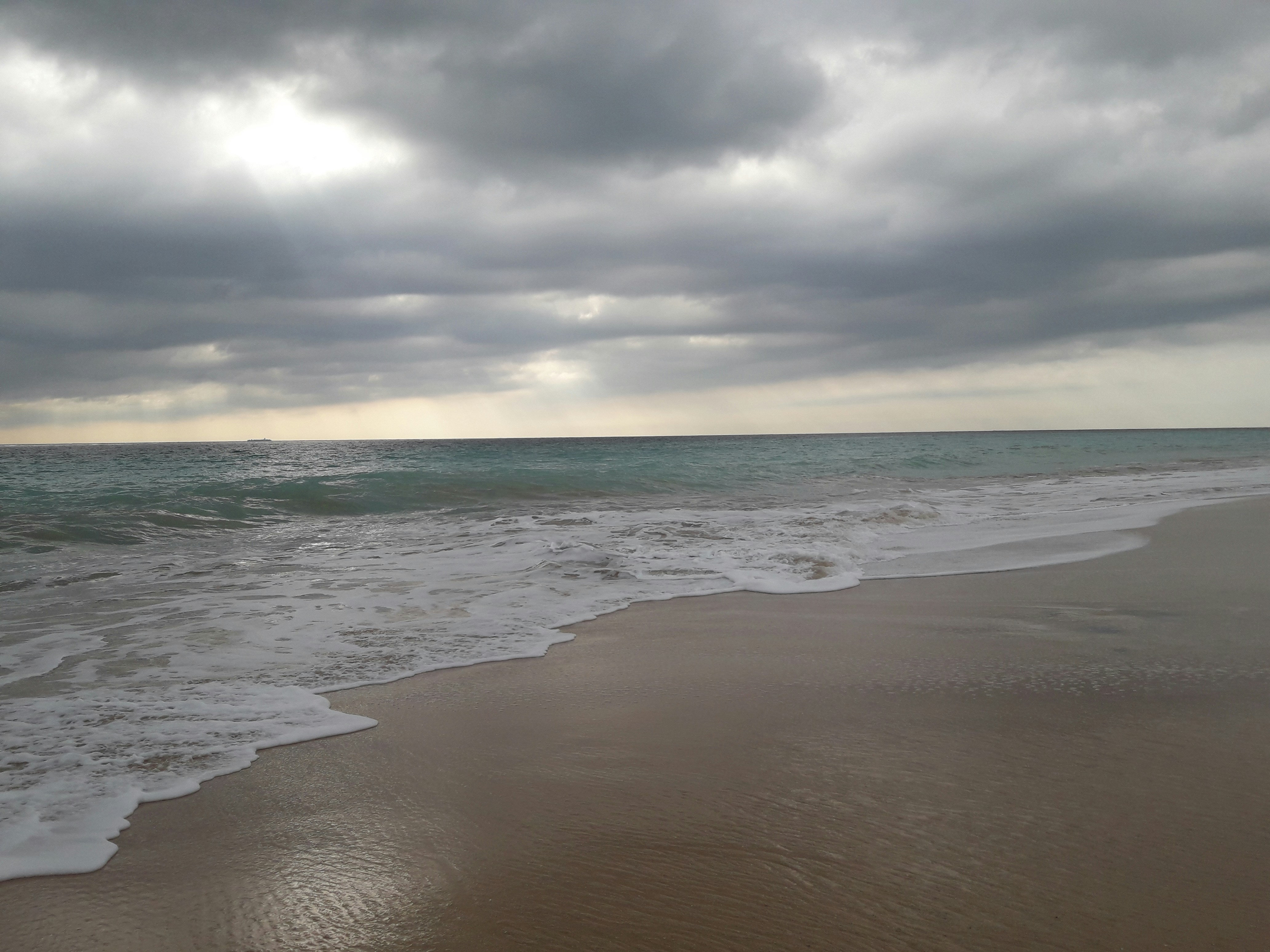 Gentle waves lapping at a sandy shore beneath a dramatic sky, evoking a sense of tranquility and introspection.